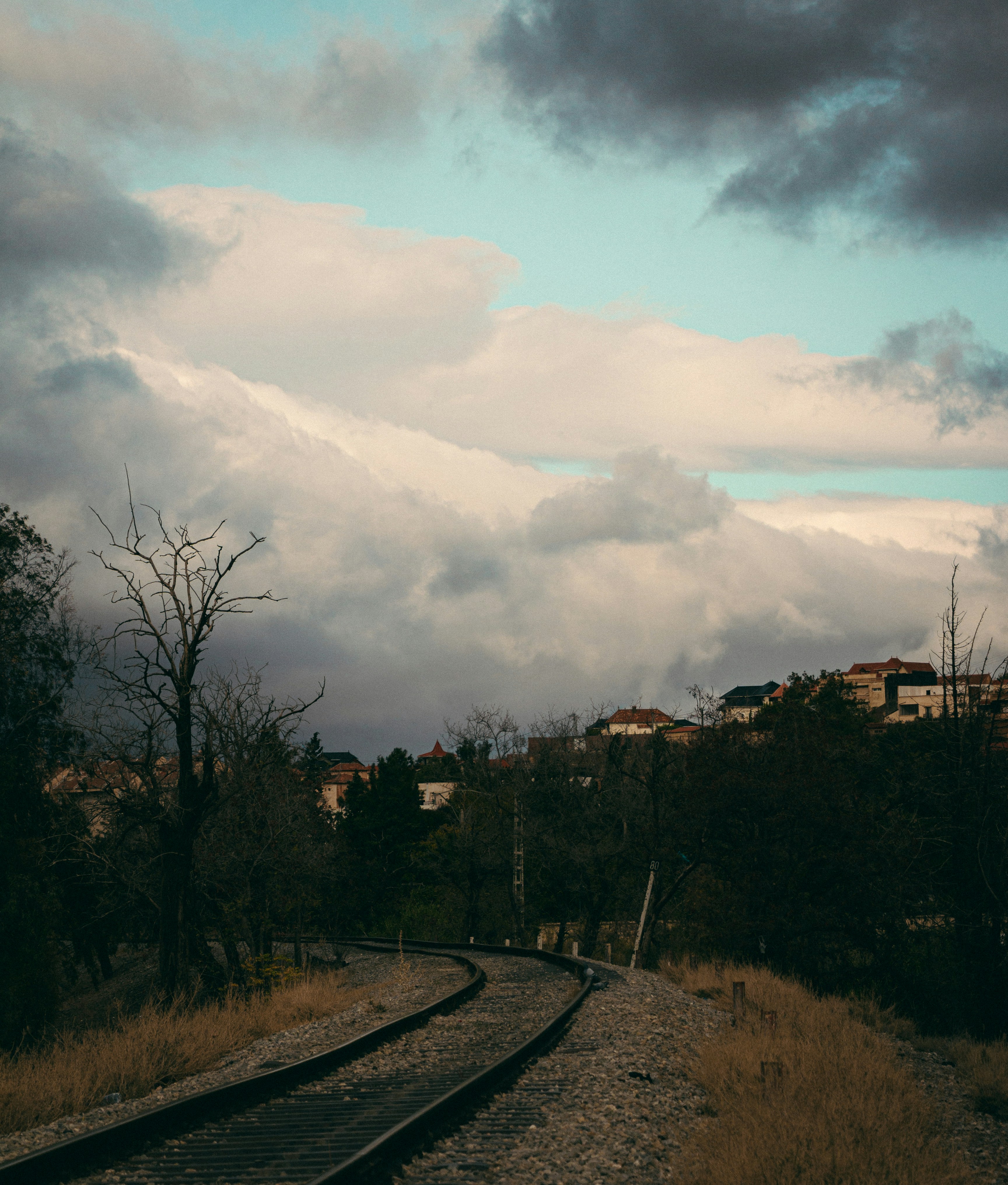 Curved Rails Toward a Hillside Town Under a Cloudy Sky