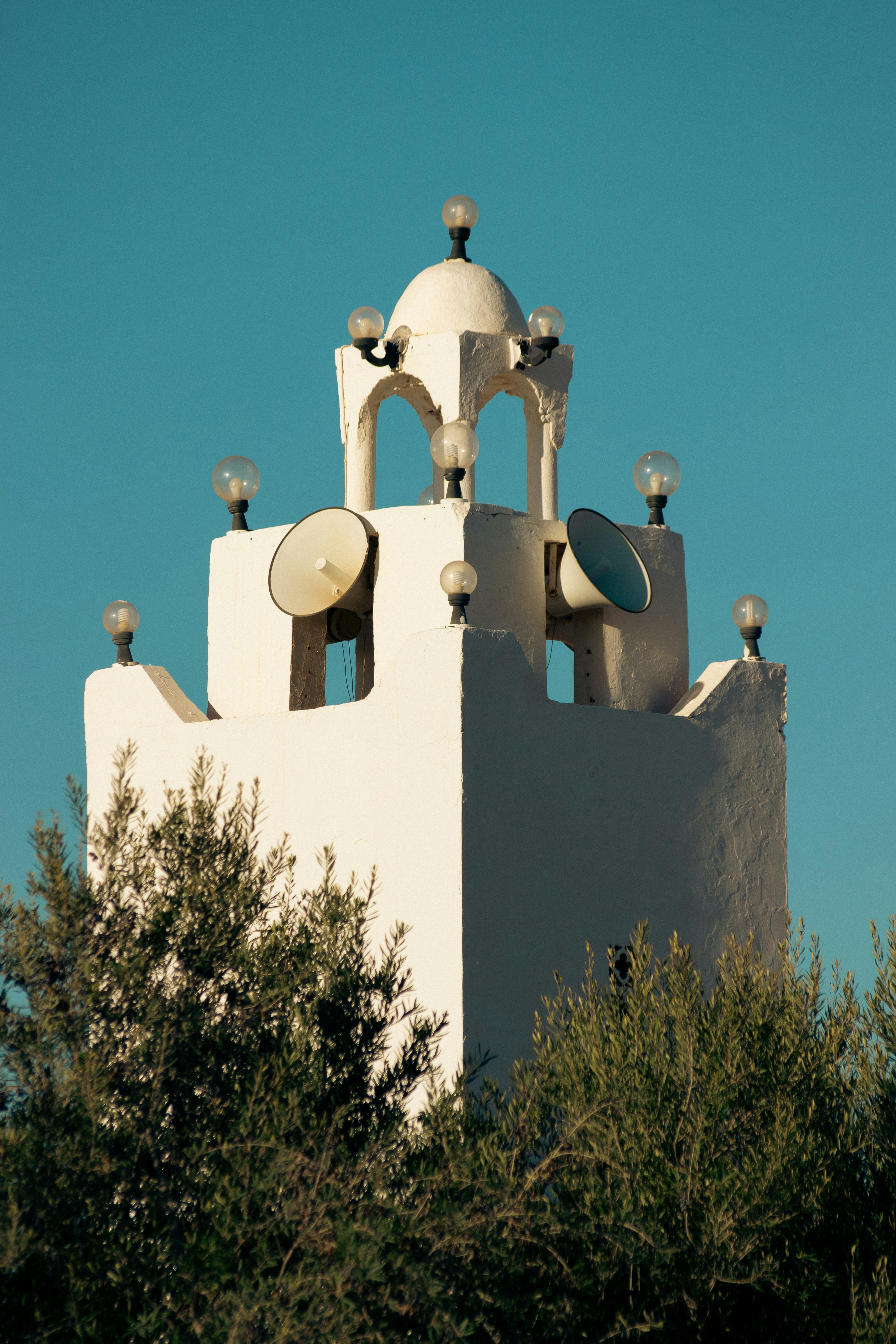 A white minaret of a mosque in Djerba, standing tall amidst a grove of olive trees. This captivating image epitomizes the harmony between nature and religious architecture.