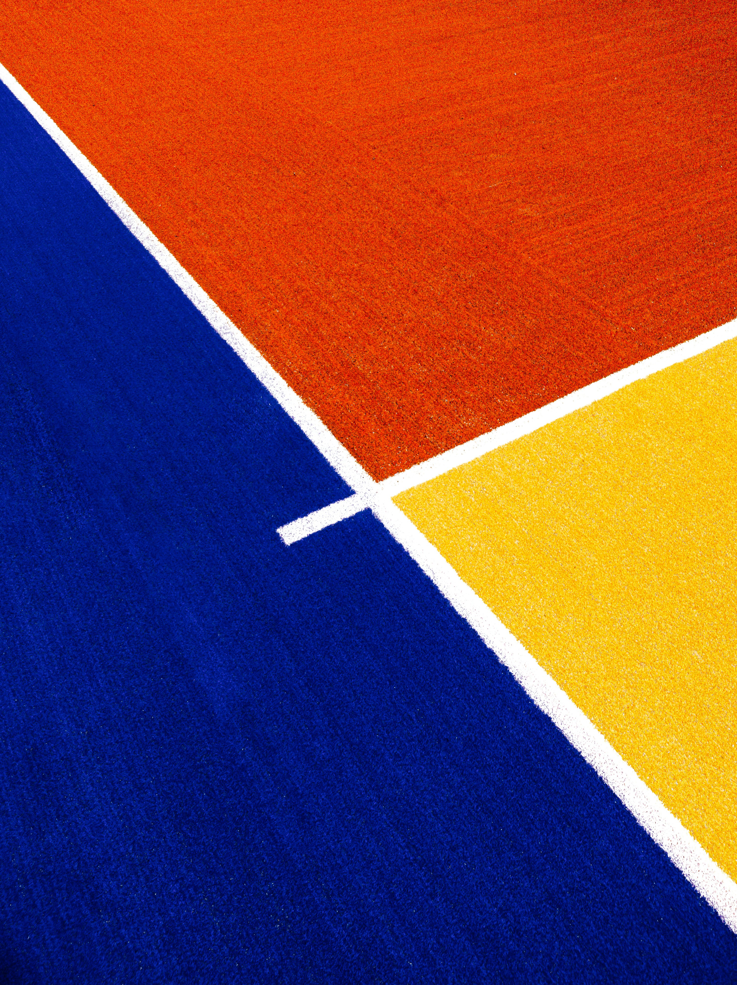 Close-up photograph of a geometric painted surface on a court, featuring bold blue, orange, and yellow sections separated by crisp white lines.