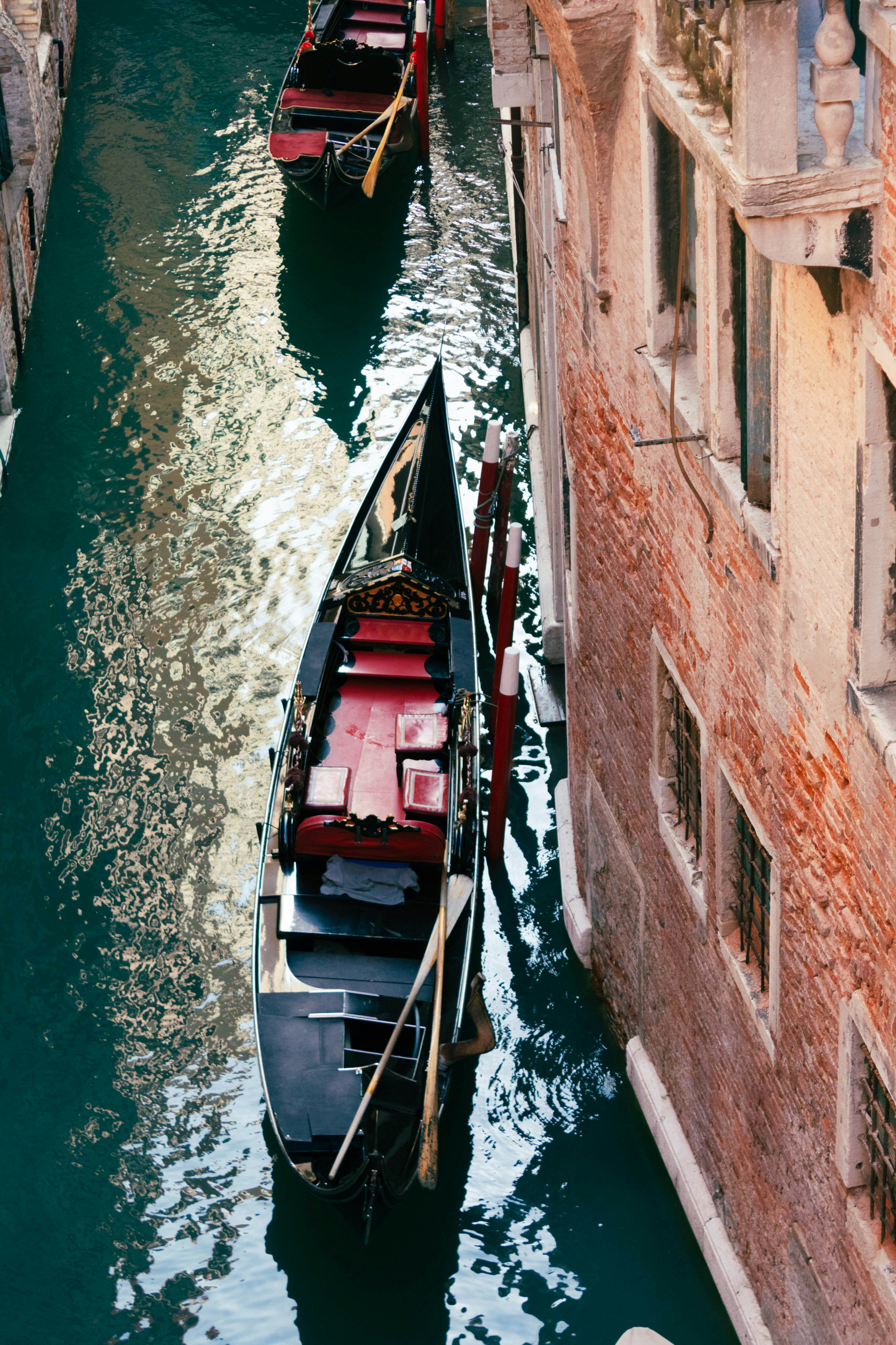 Two gondolas glide through a narrow Venetian canal, flanked by weathered brick buildings reflecting in the water.