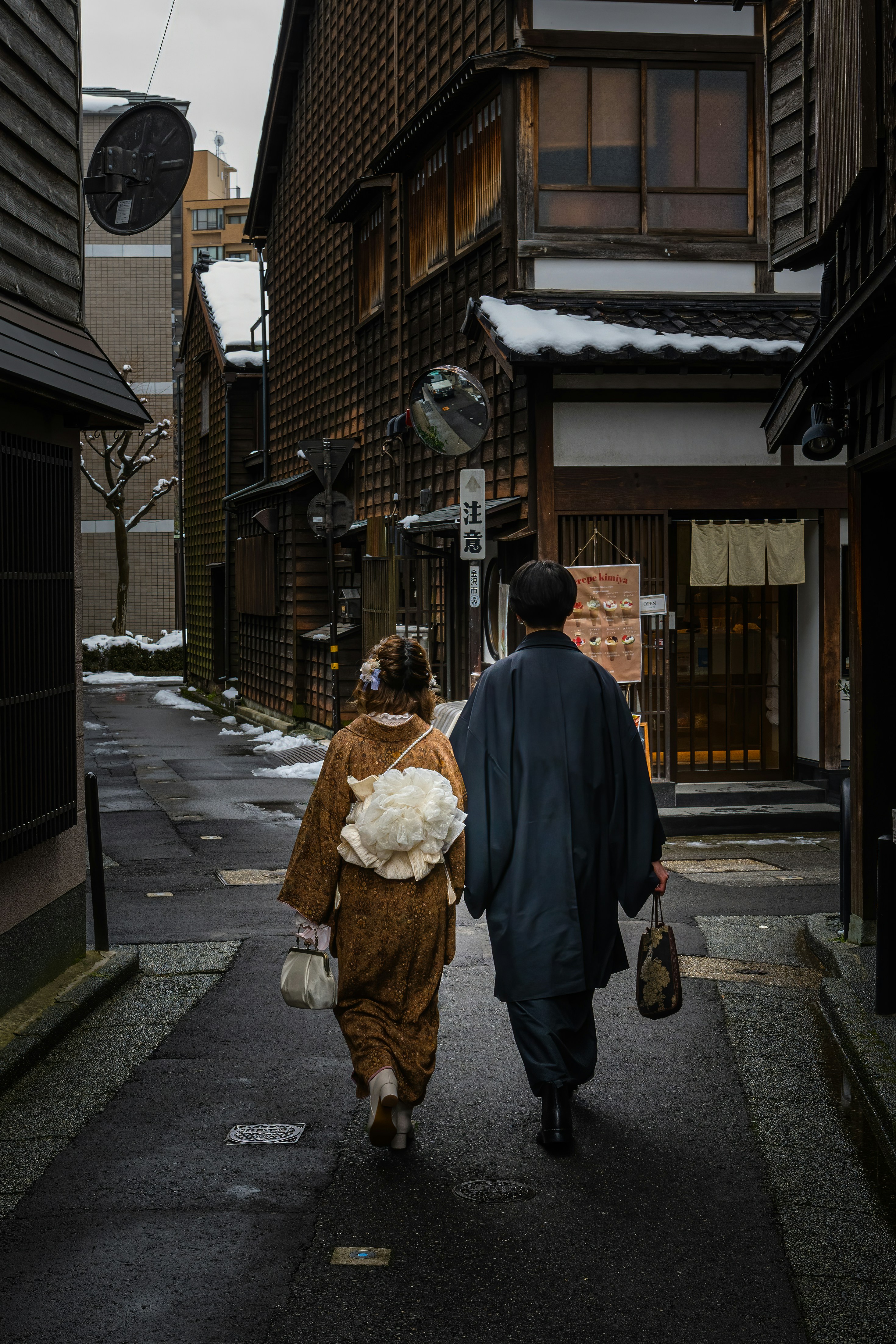 A young couple enjoying dressing up in traditional clothes and exploring the historic, well-preserved teahouse and geisha streets of the Higashi Chaya District in Kanazawa, Japan during chilly winter. | a couple of people walking down a street