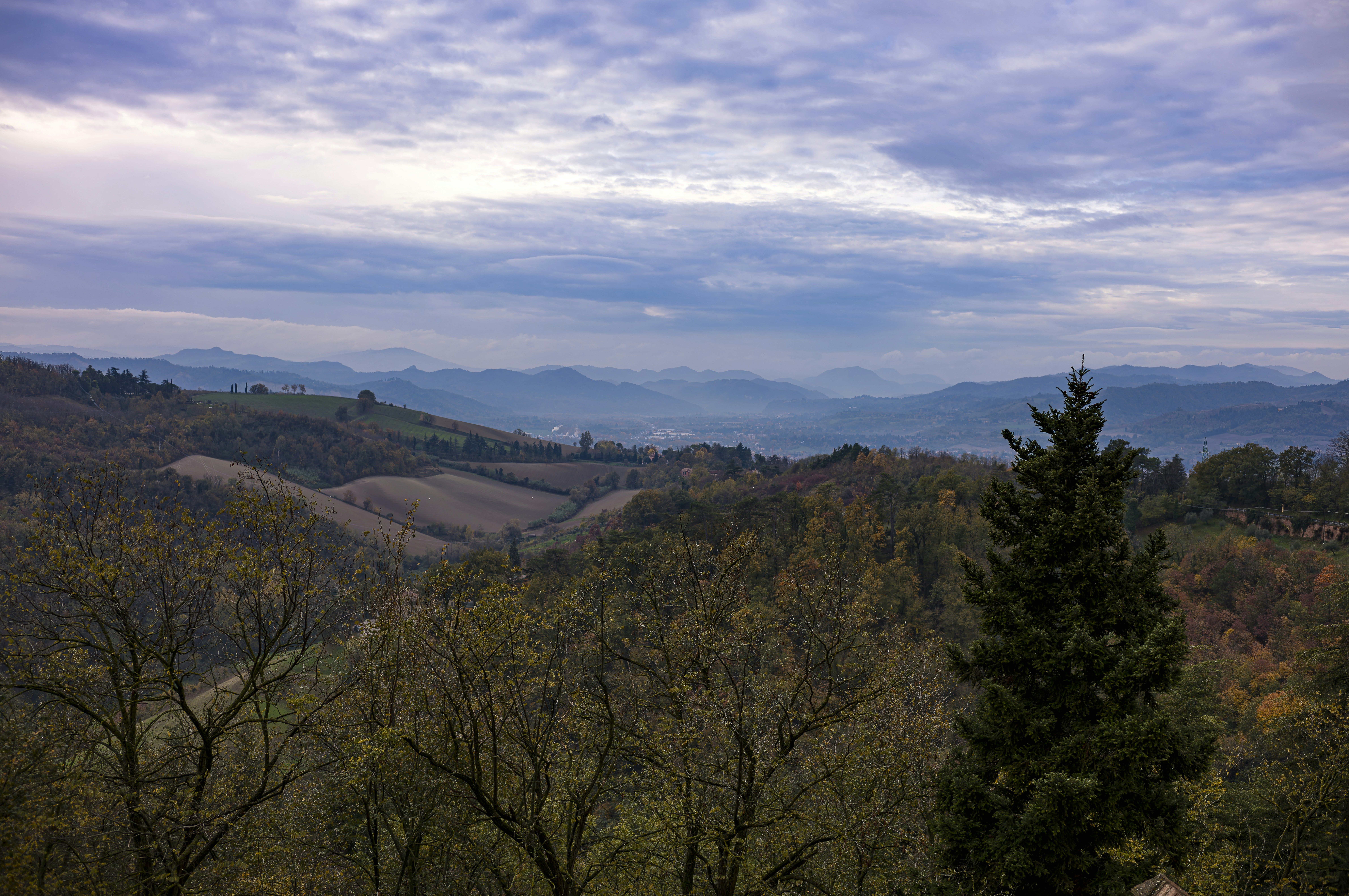 Rolling hills under a cloudy sky with autumn foliage in Emilia Romagna.