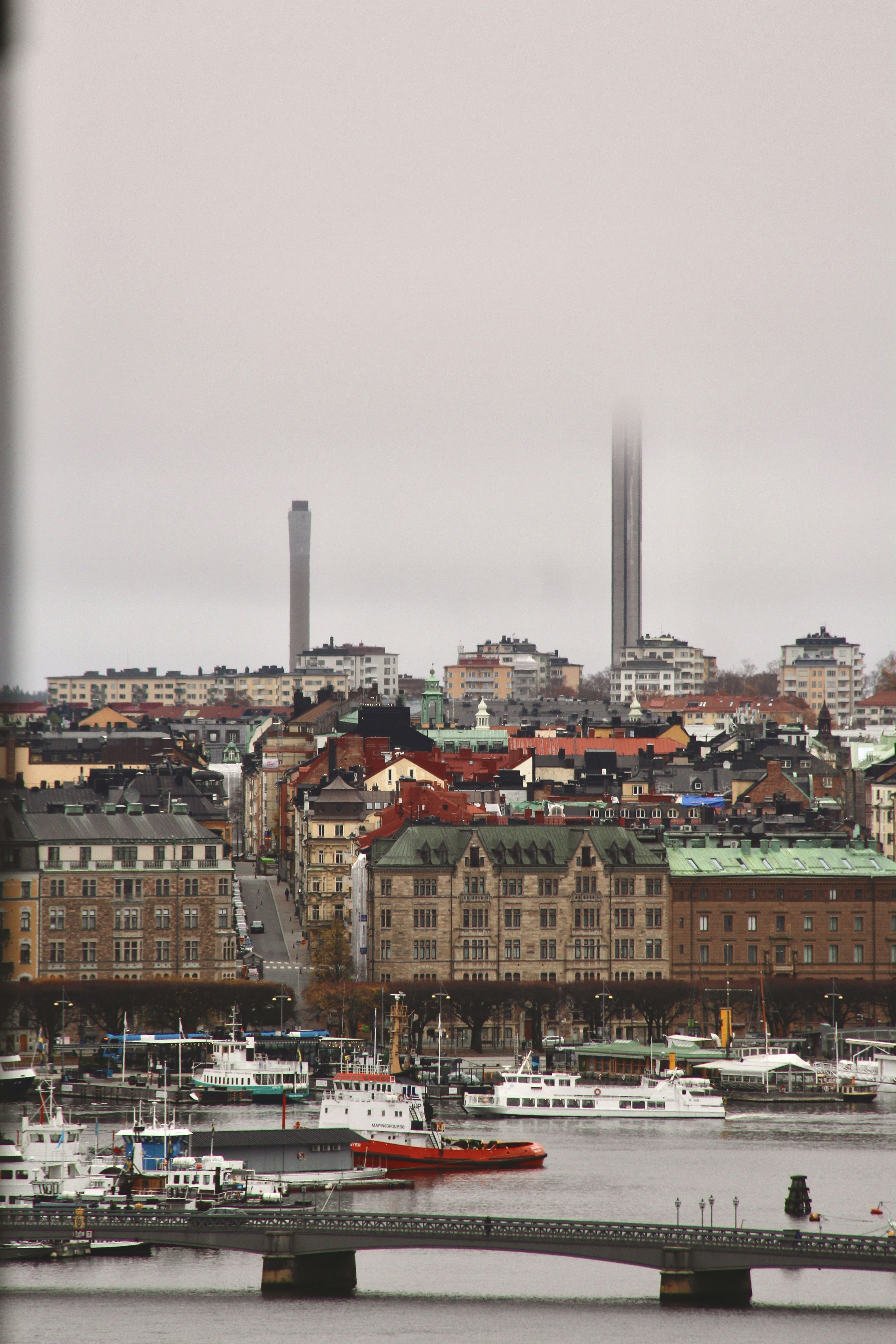 Twin Smokestacks Over a Waterfront Cityscape: Boats, Bridge, and Brick Facades