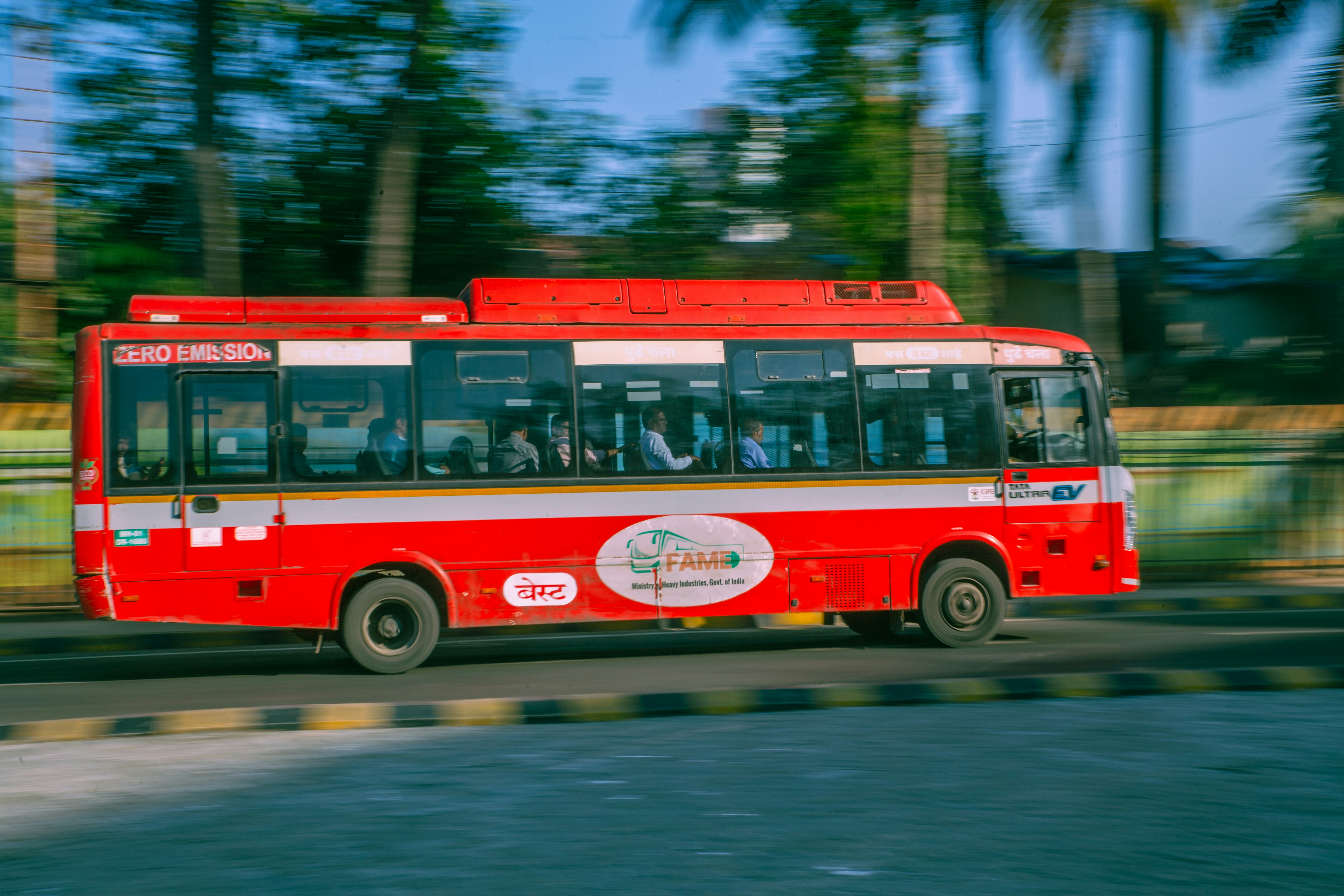A red bus driving down a street next to a forest photo – Free Human ...