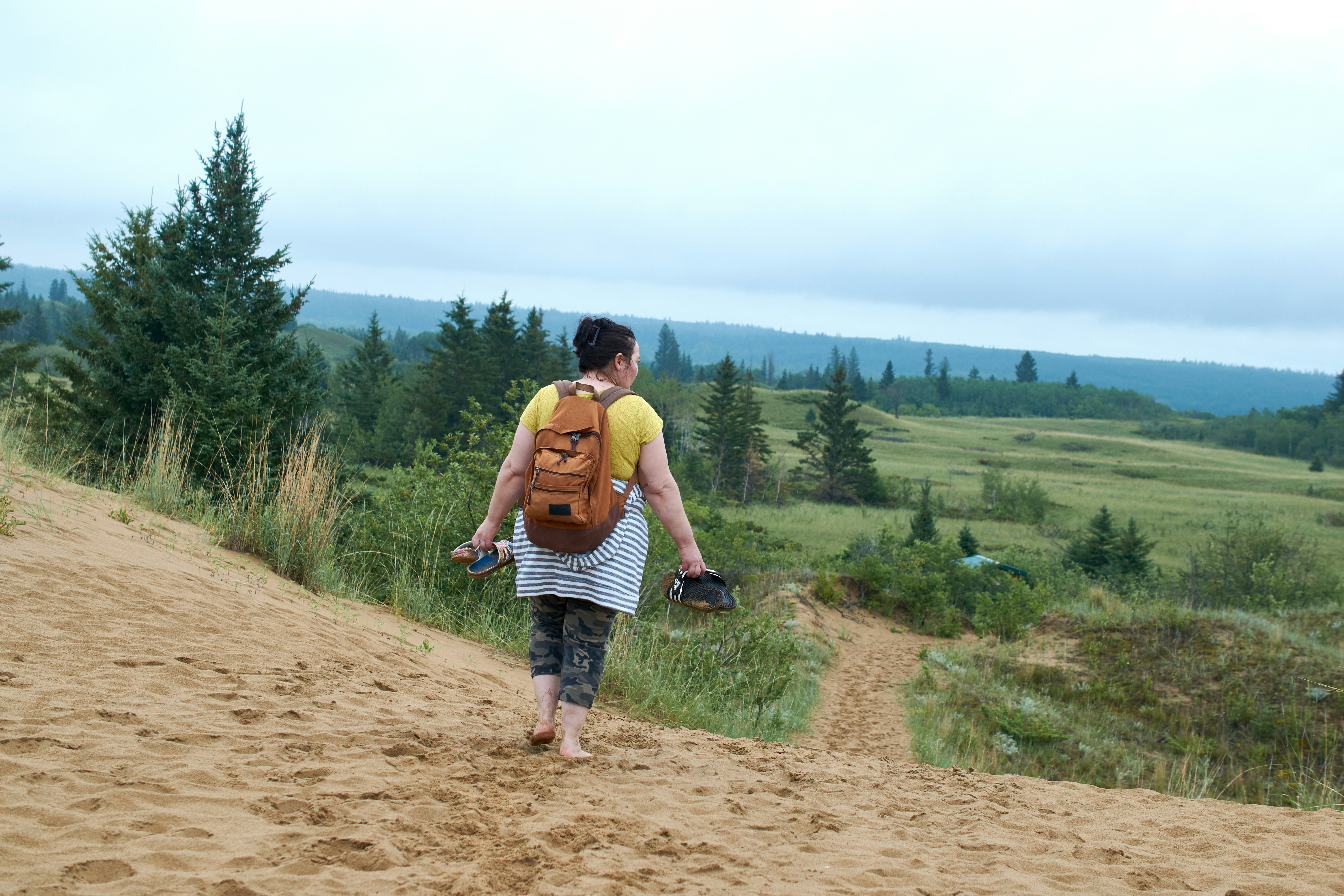 Trail Warrior: A Lone Hiker Descends a Sandy Ridge Toward Verdant Horizons