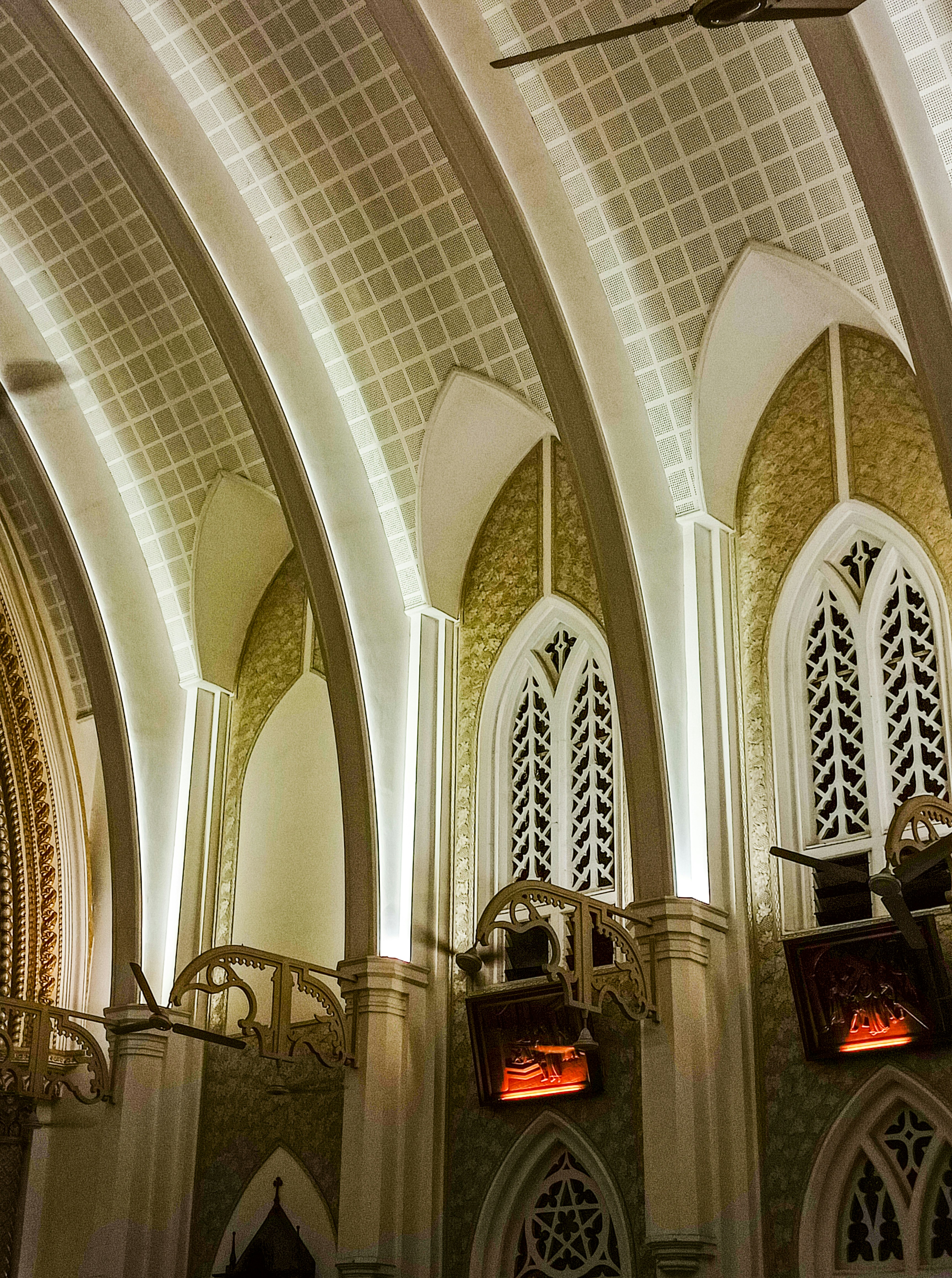 Interior shot of a cathedral arcade bathed in warm artificial light, highlighting ribbed vaults and ornate windows.
