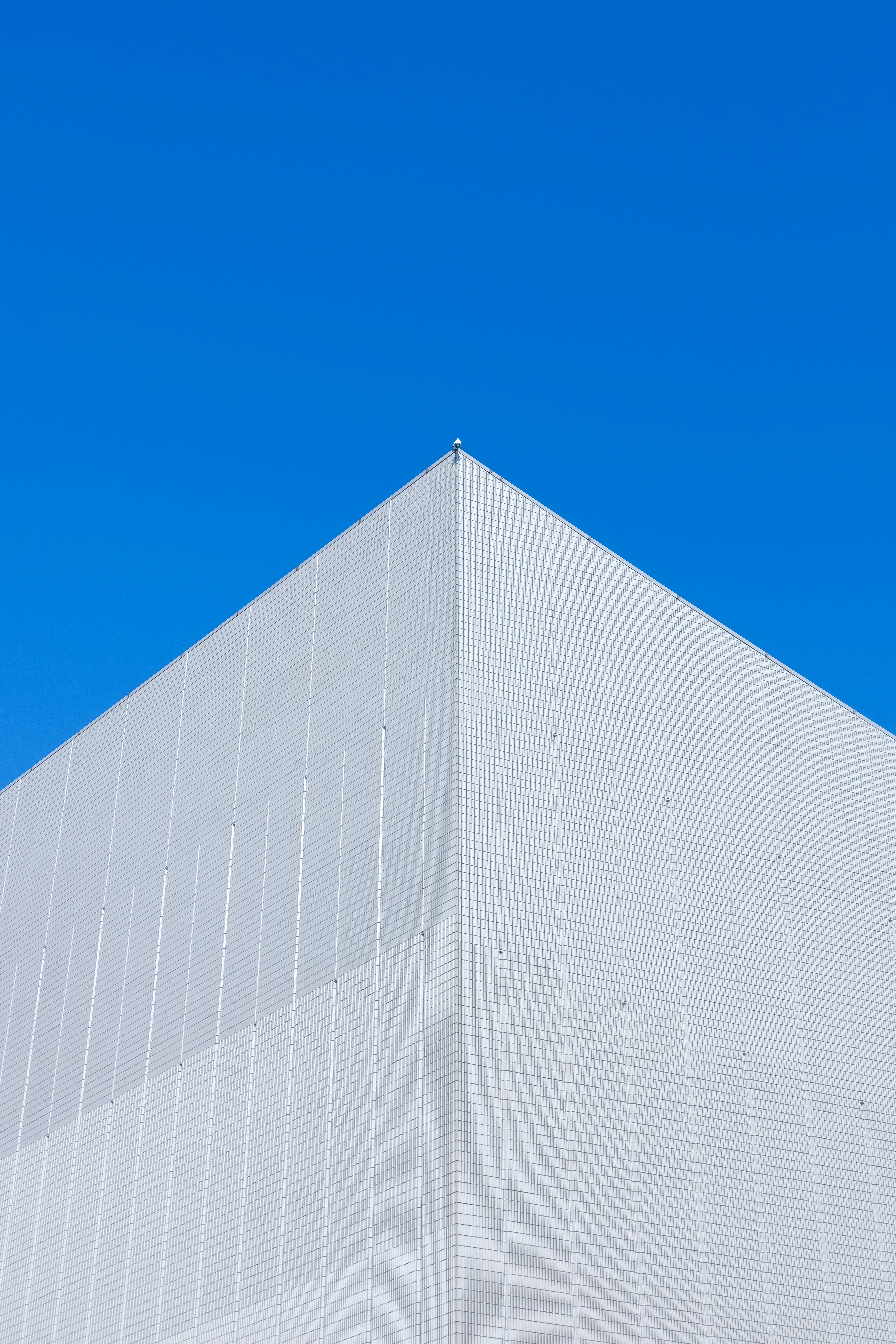 A minimalist architectural photograph of a white-tiled building corner set against a vivid blue sky.
