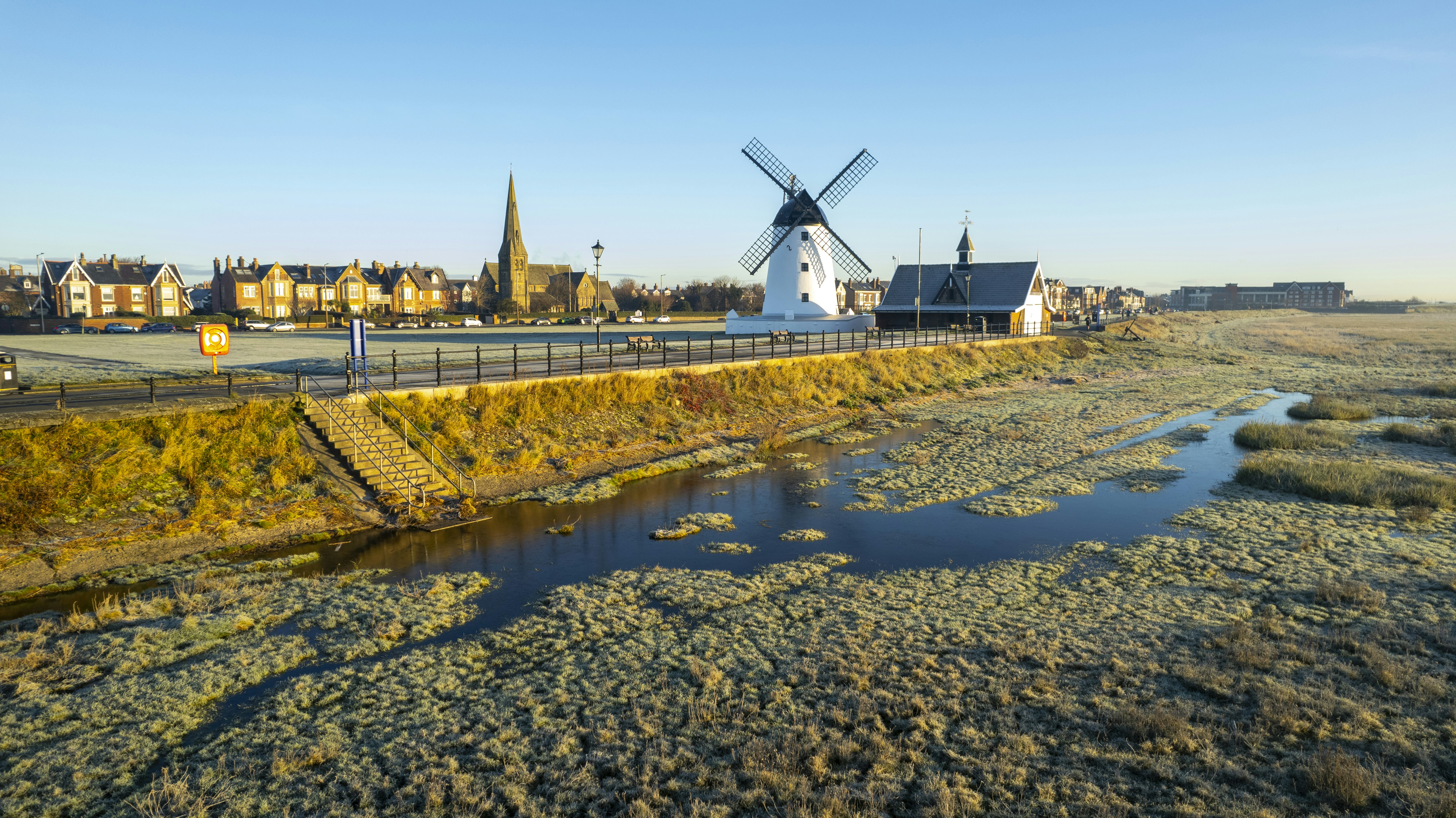 A windmill in a field next to a body of water photo – Free Lytham Image ...