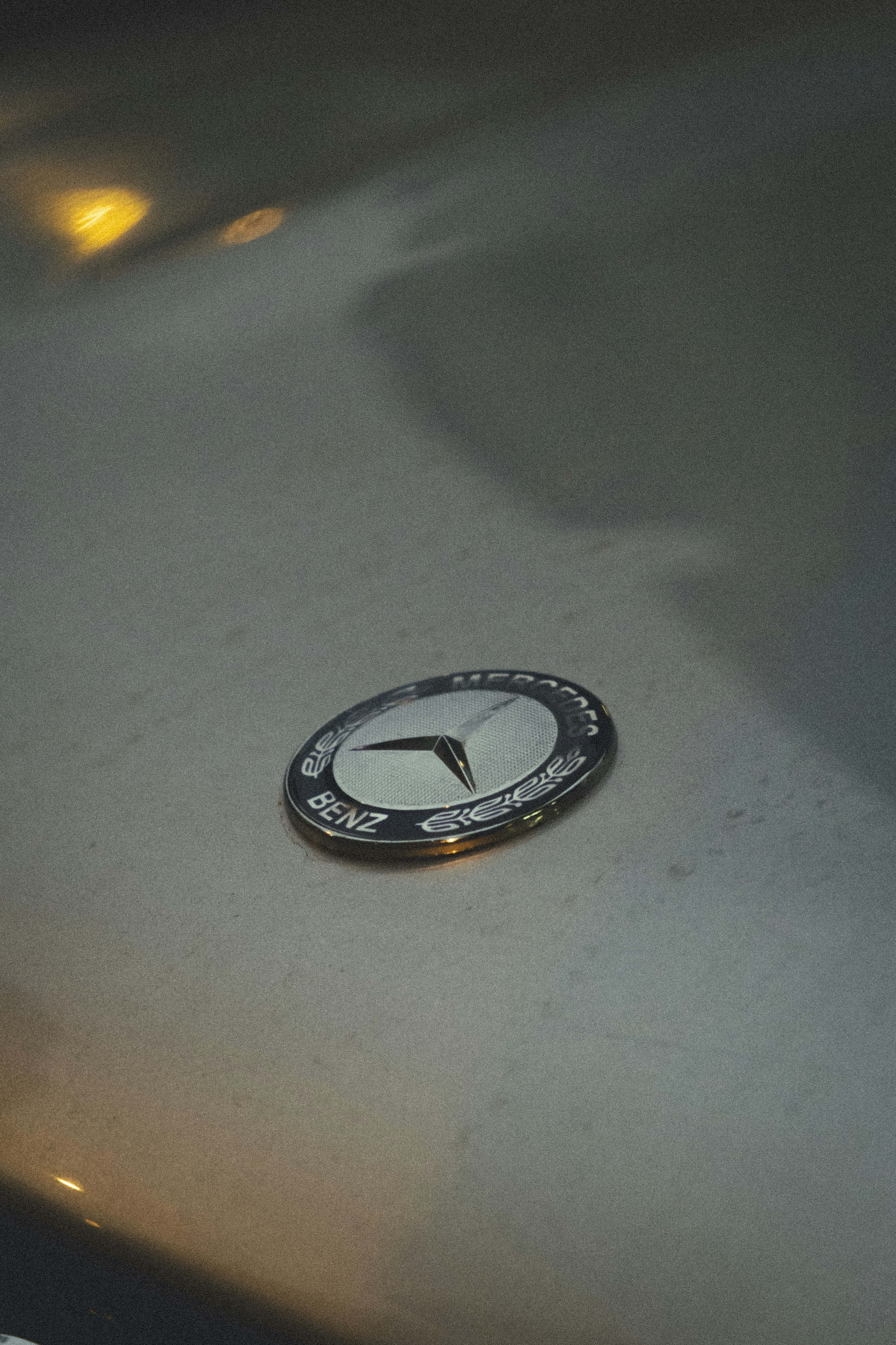 Emblem in Twilight: Mercedes-Benz badge on a dusty, dimly lit hood