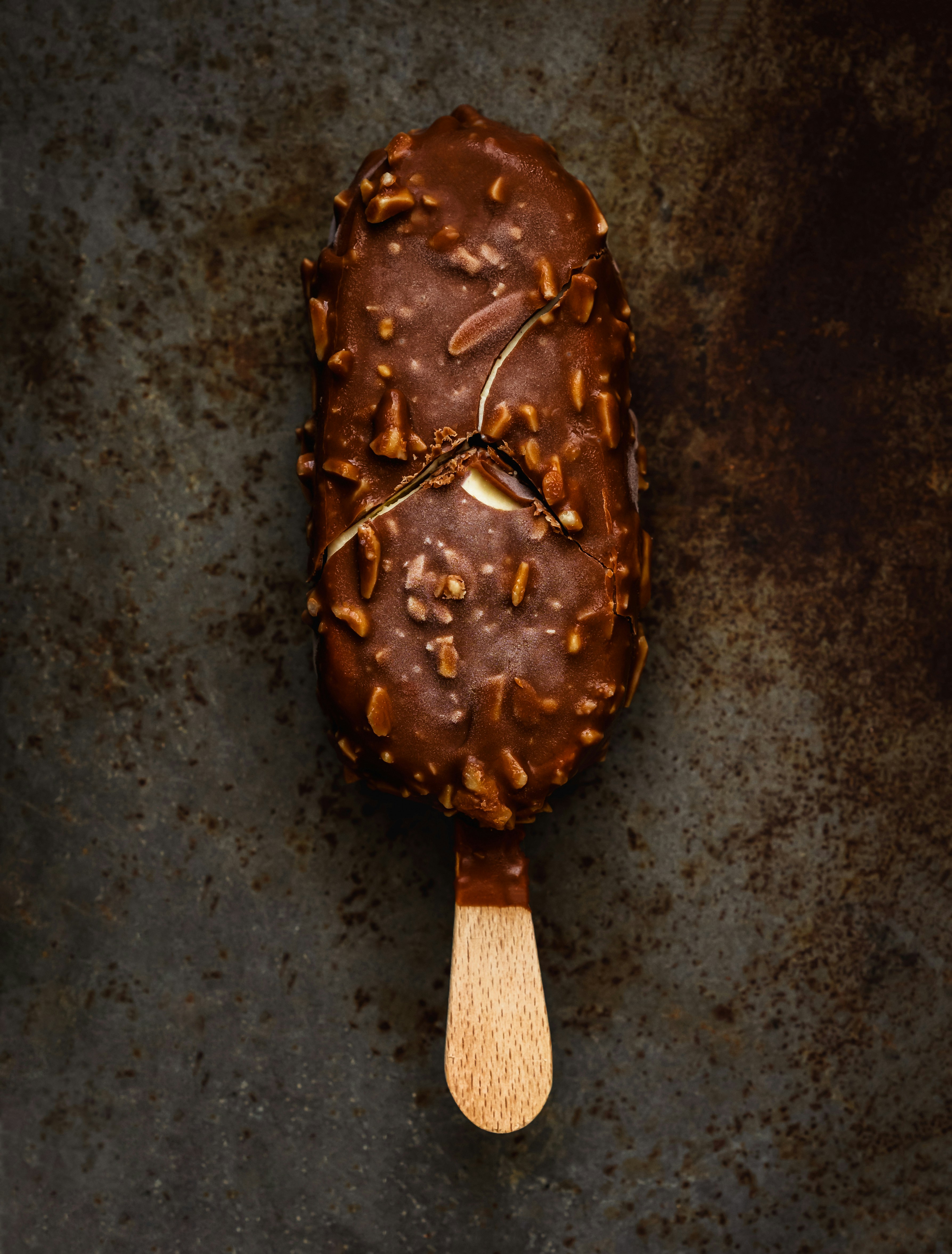 Nut-Crusted Chocolate Ice Cream Bar on a Weathered Metal Canvas