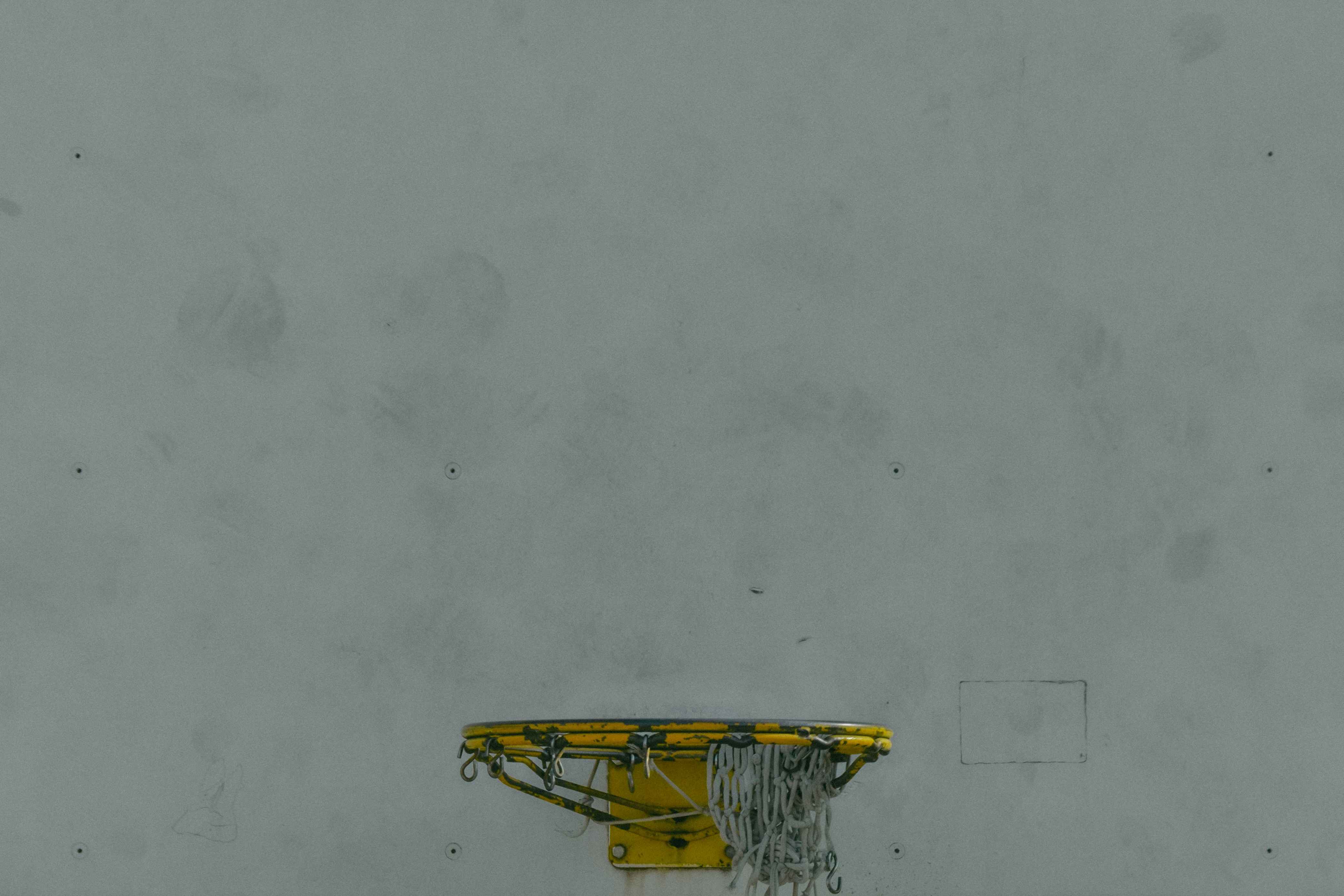 Yellow basketball hoop with chain net against a weathered concrete wall.