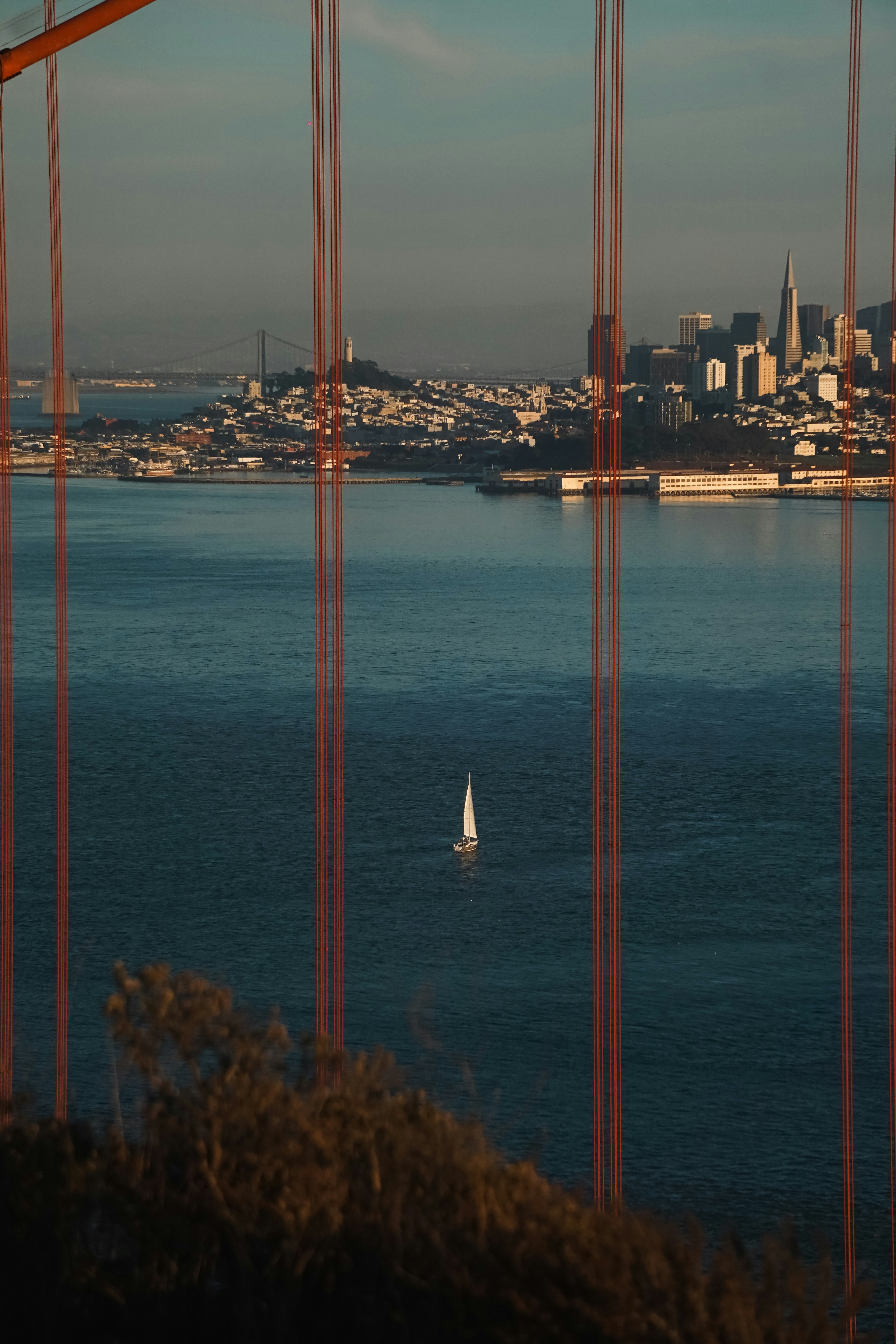Sailboat Through a Veiled Bridge: Red Cables Framing San Francisco Bay