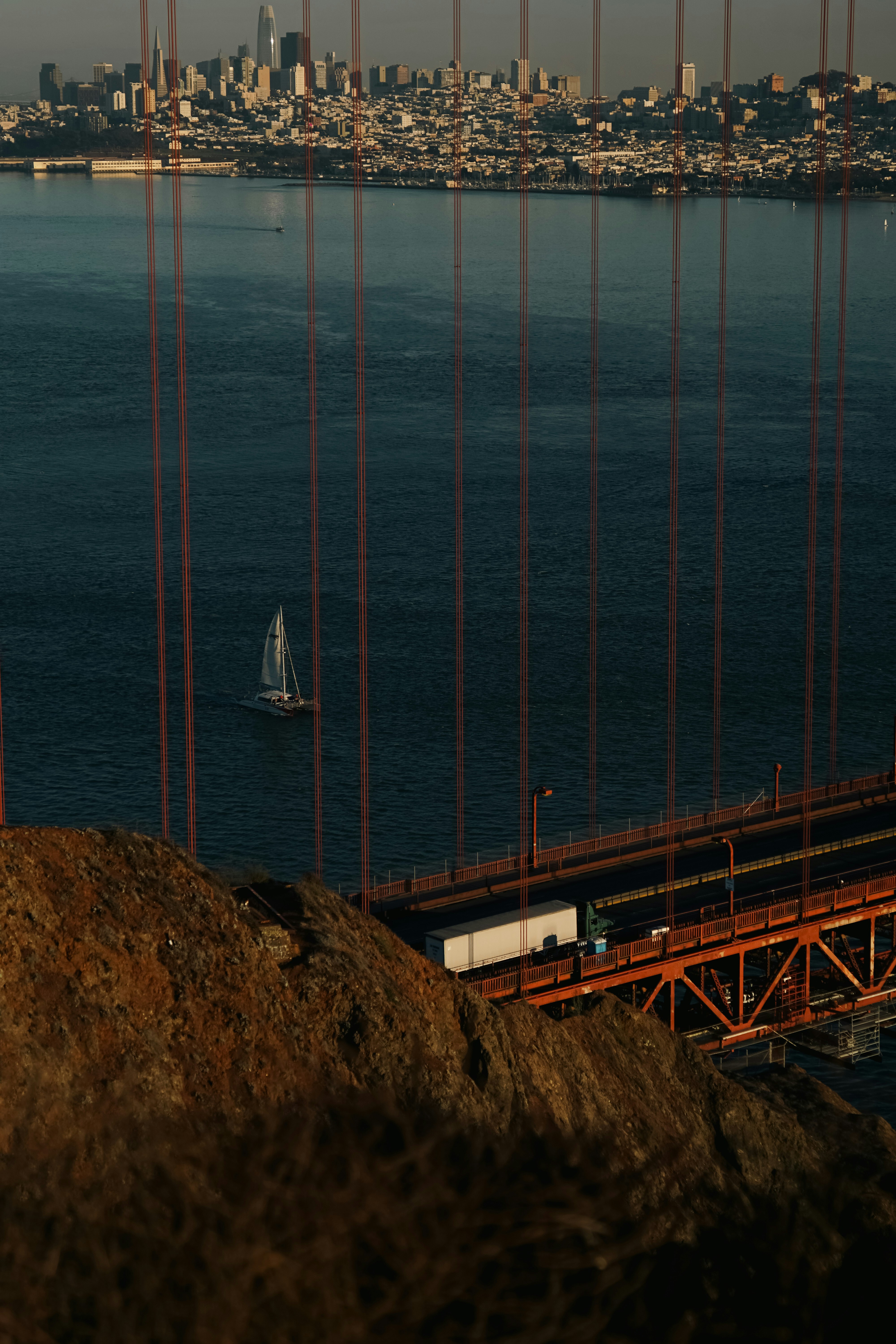 Sailboat in a Bay Glimpse: City Lights Beyond a Fiery Red Bridge
