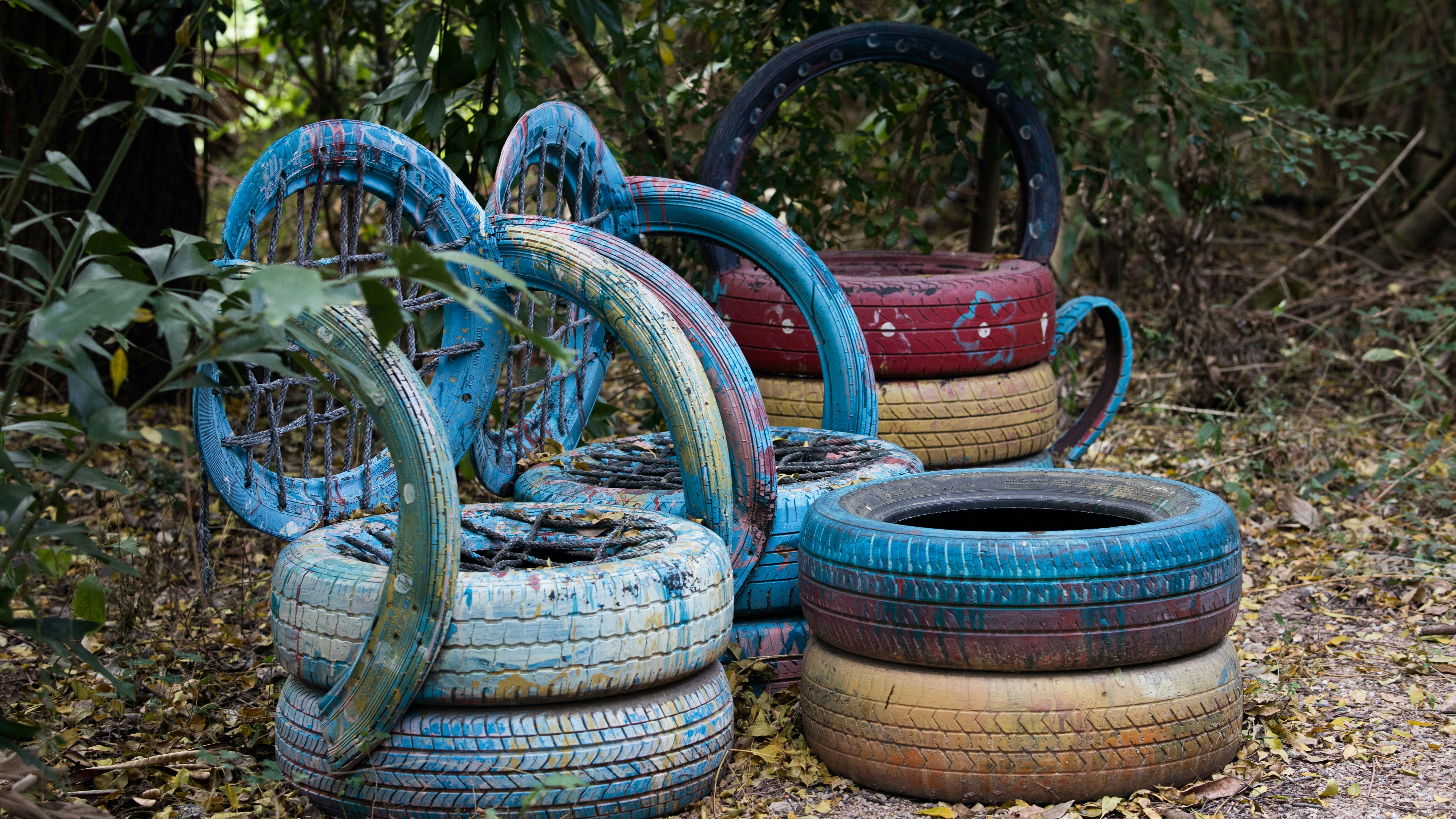 Colorfully painted tires arranged artistically in a natural setting, showcasing innovative recycling. The vibrant hues contrast with the surrounding greenery.