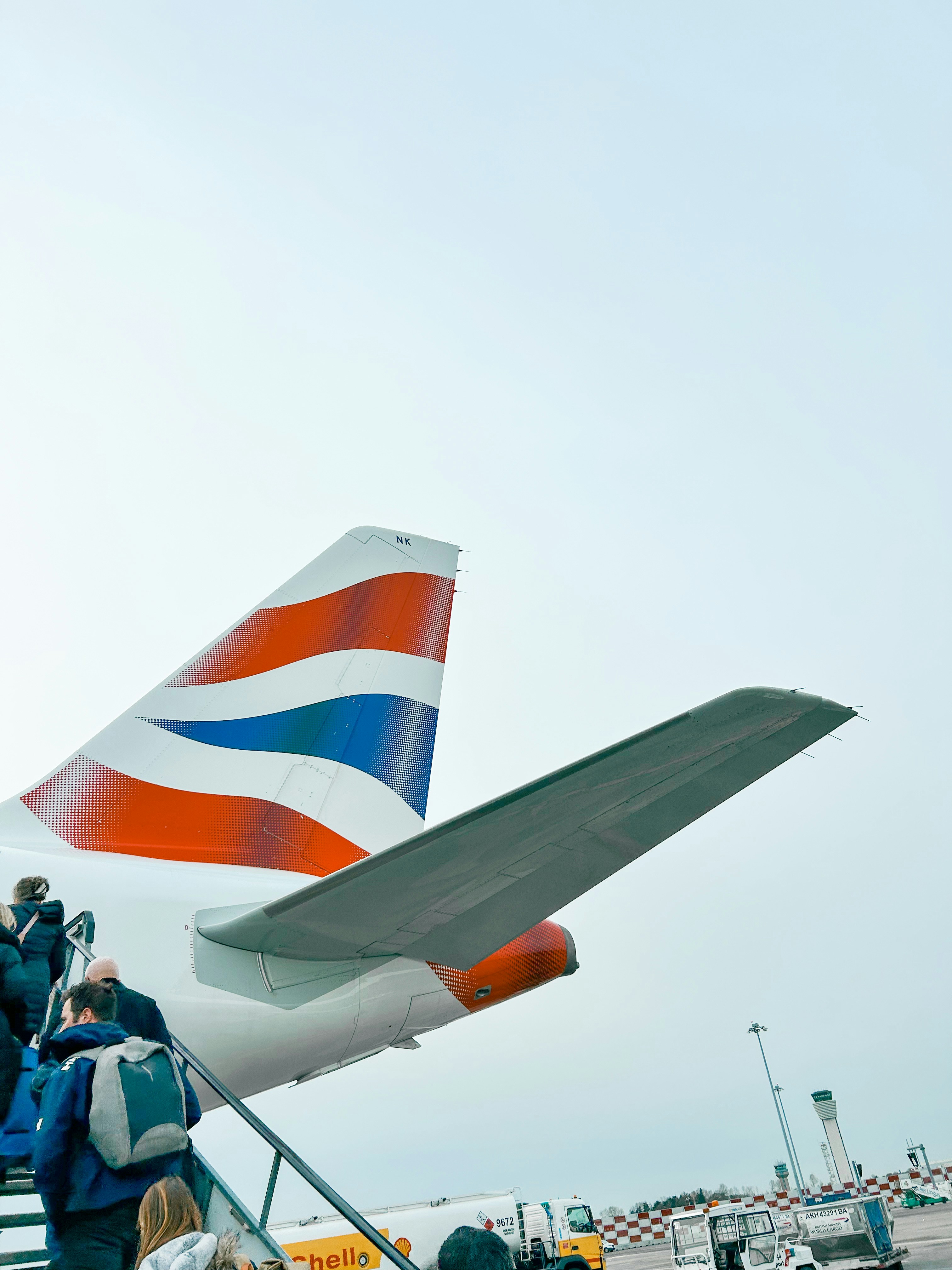Passengers boarding a British Airways aircraft, highlighting the iconic tail design against a pale sky.