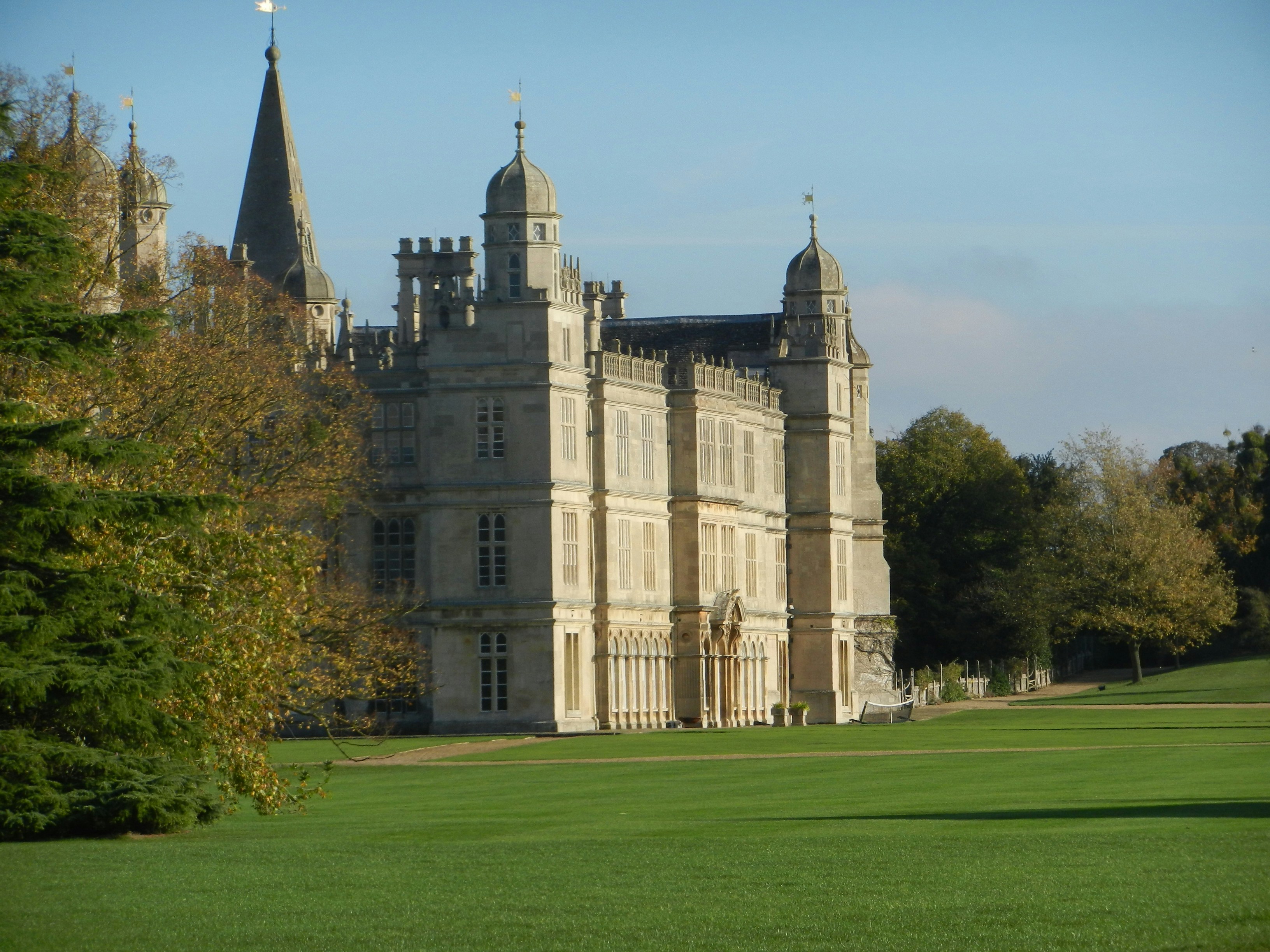 Historic stone manor with clock tower surrounded by lush green lawn and autumn trees.