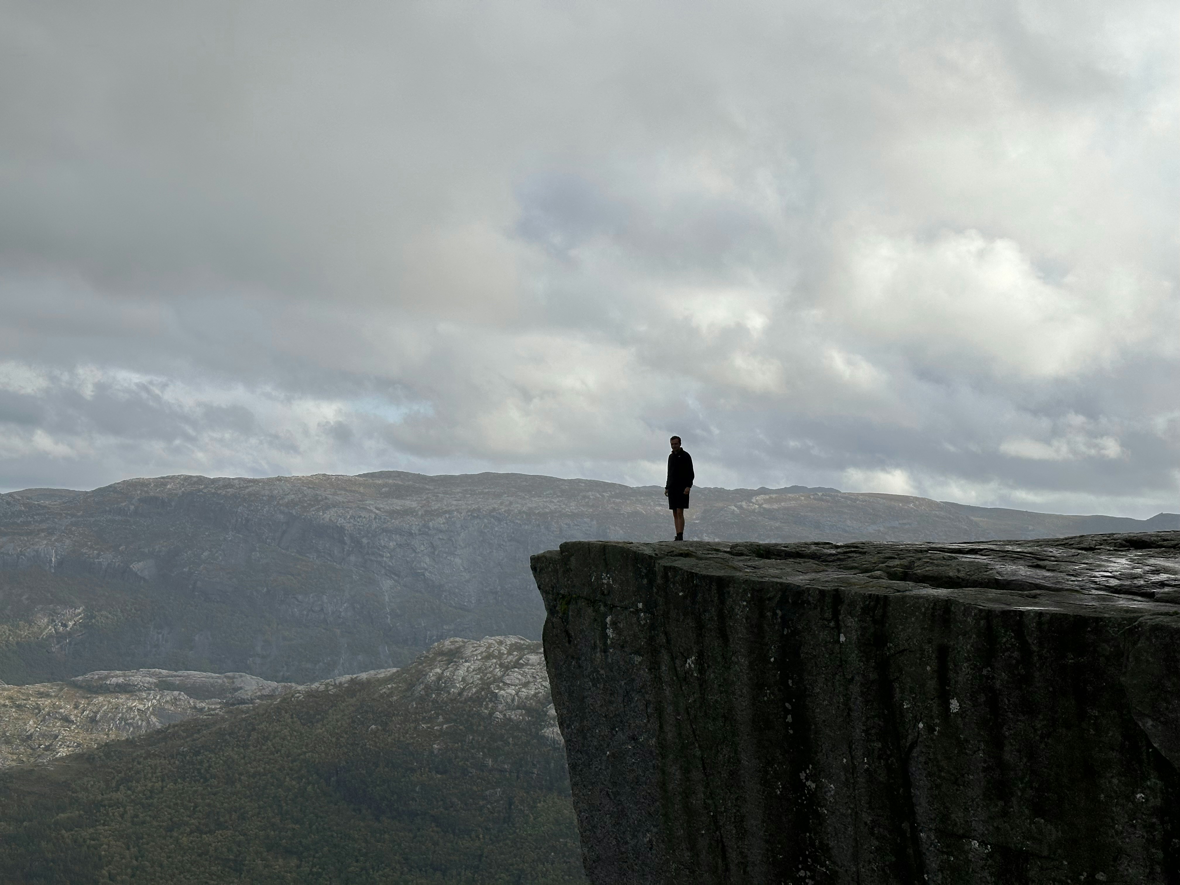 Person standing alone at the edge of a dramatic cliff under a cloudy sky.