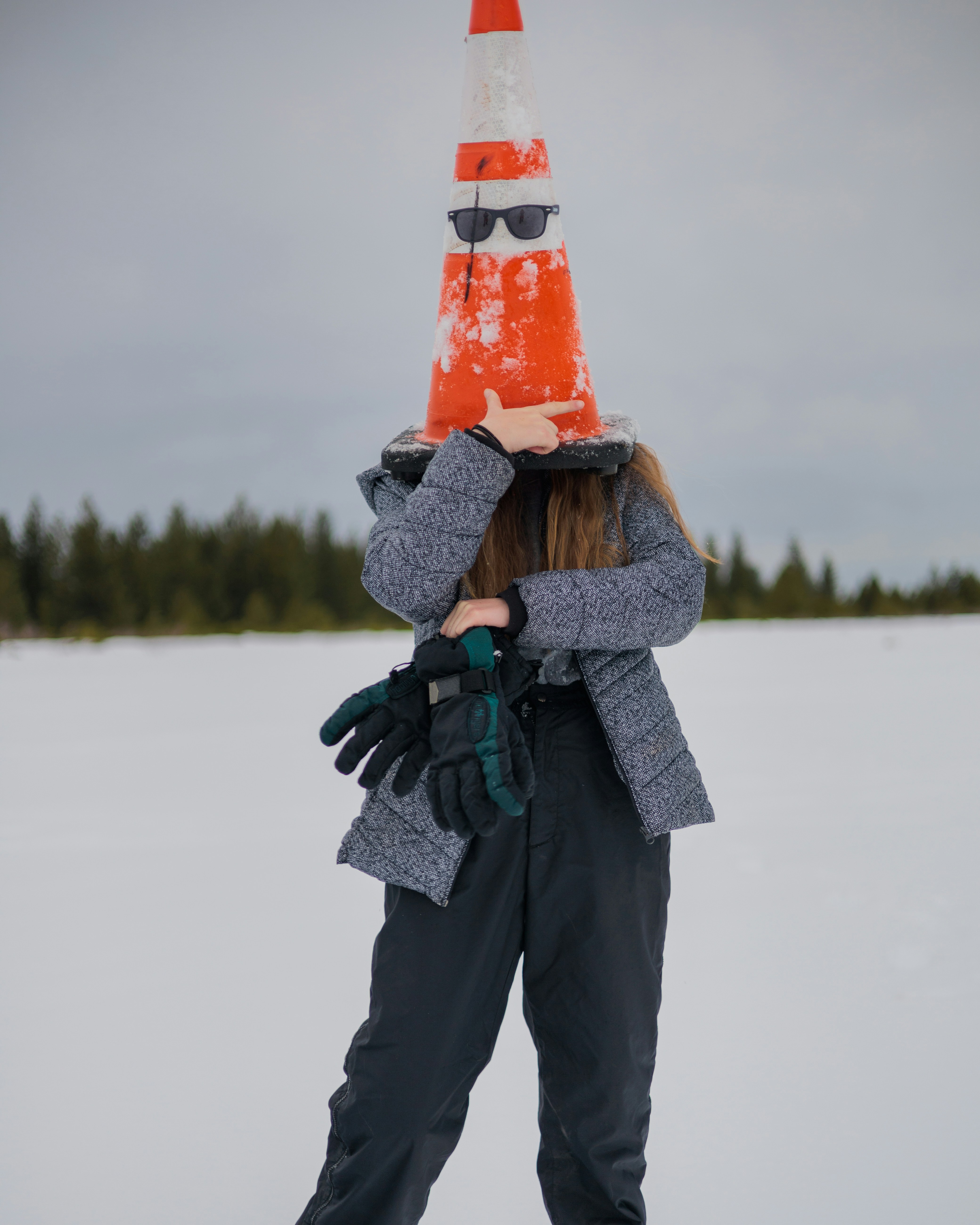 A woman standing in the snow with a red and white traffic cone on her ...