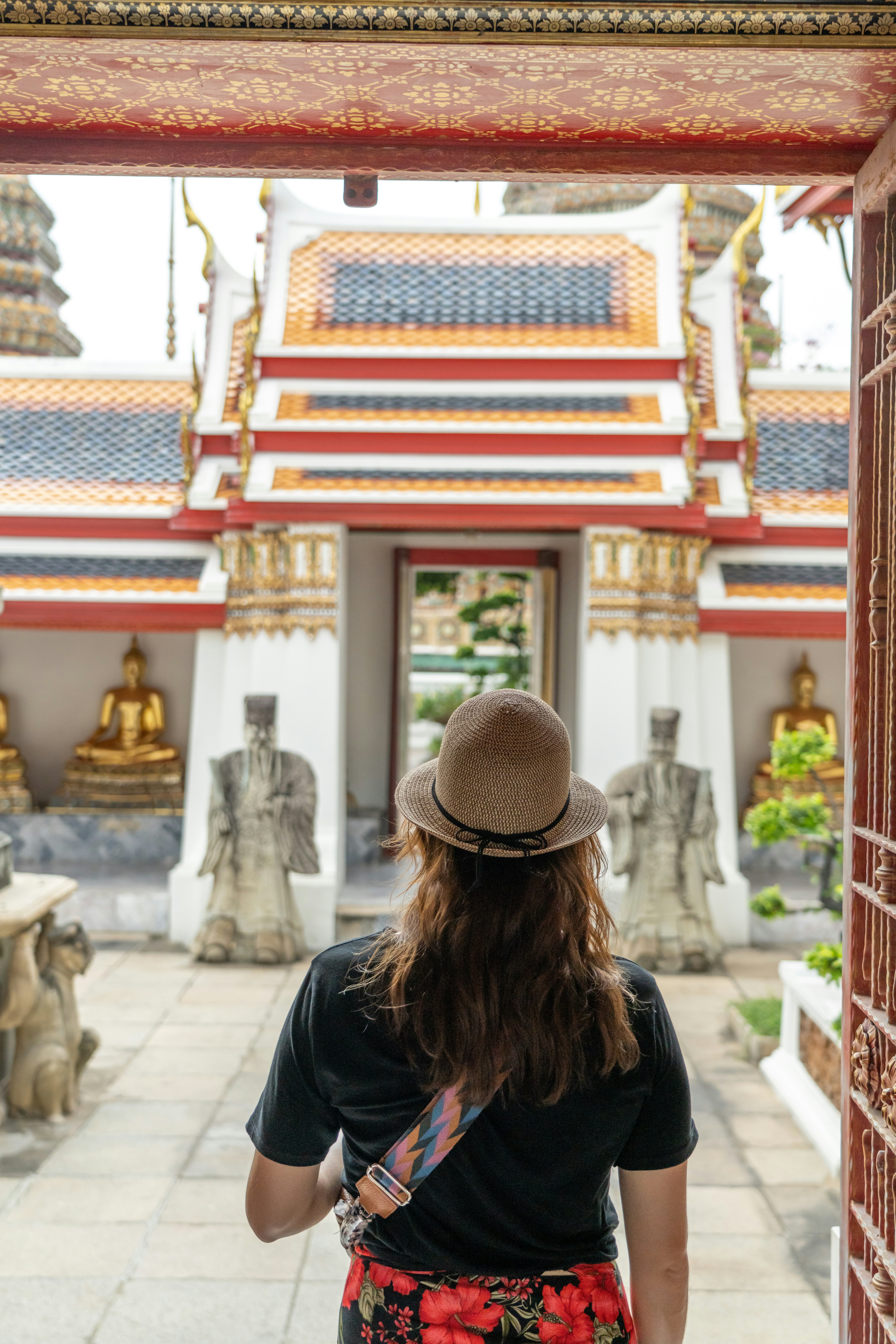 Back to the Gate: A Traveler in the Temple Courtyard Framed by Buddha Statues