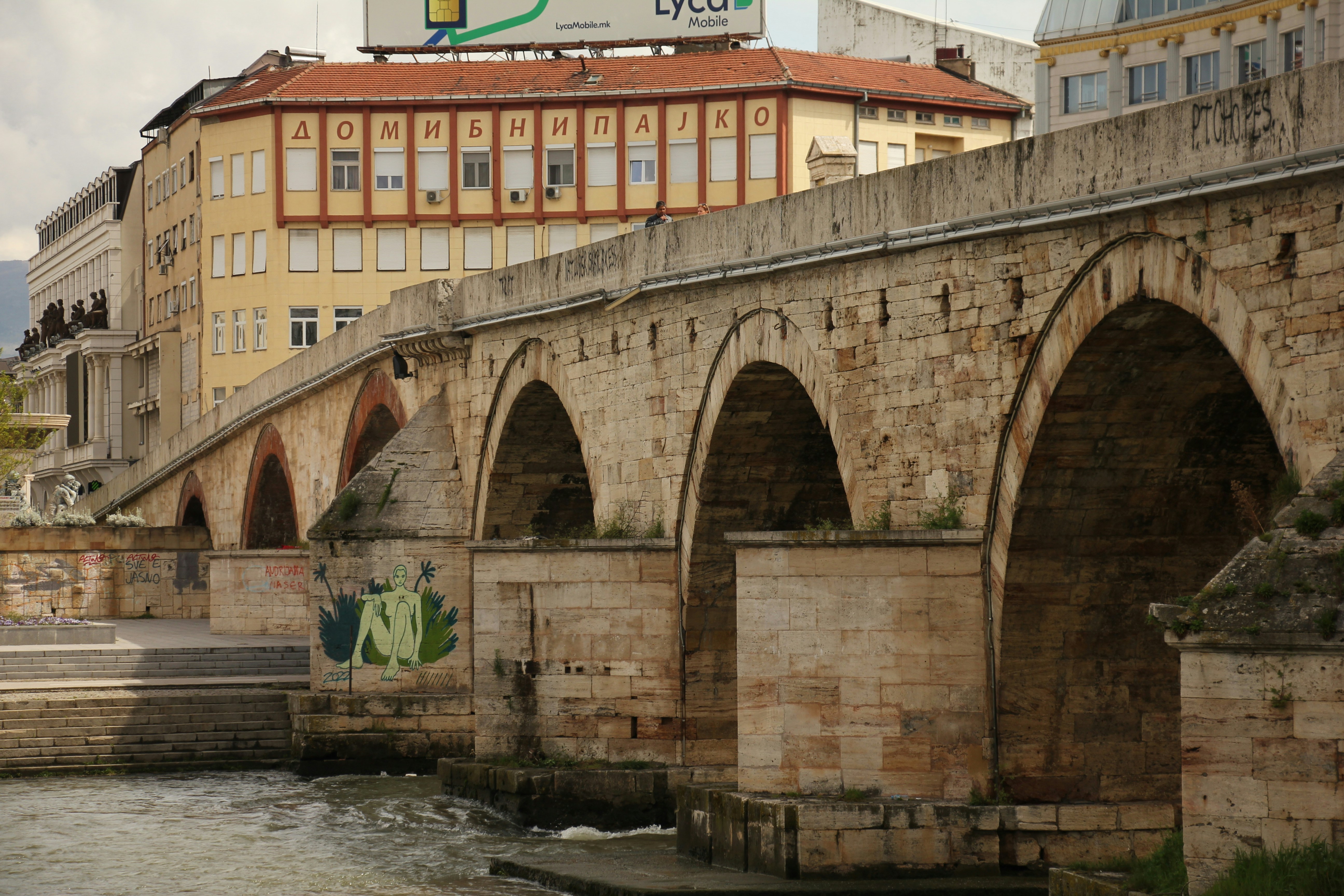 Stone Arch Rhythm Over a Quiet River: City Facades in the Background