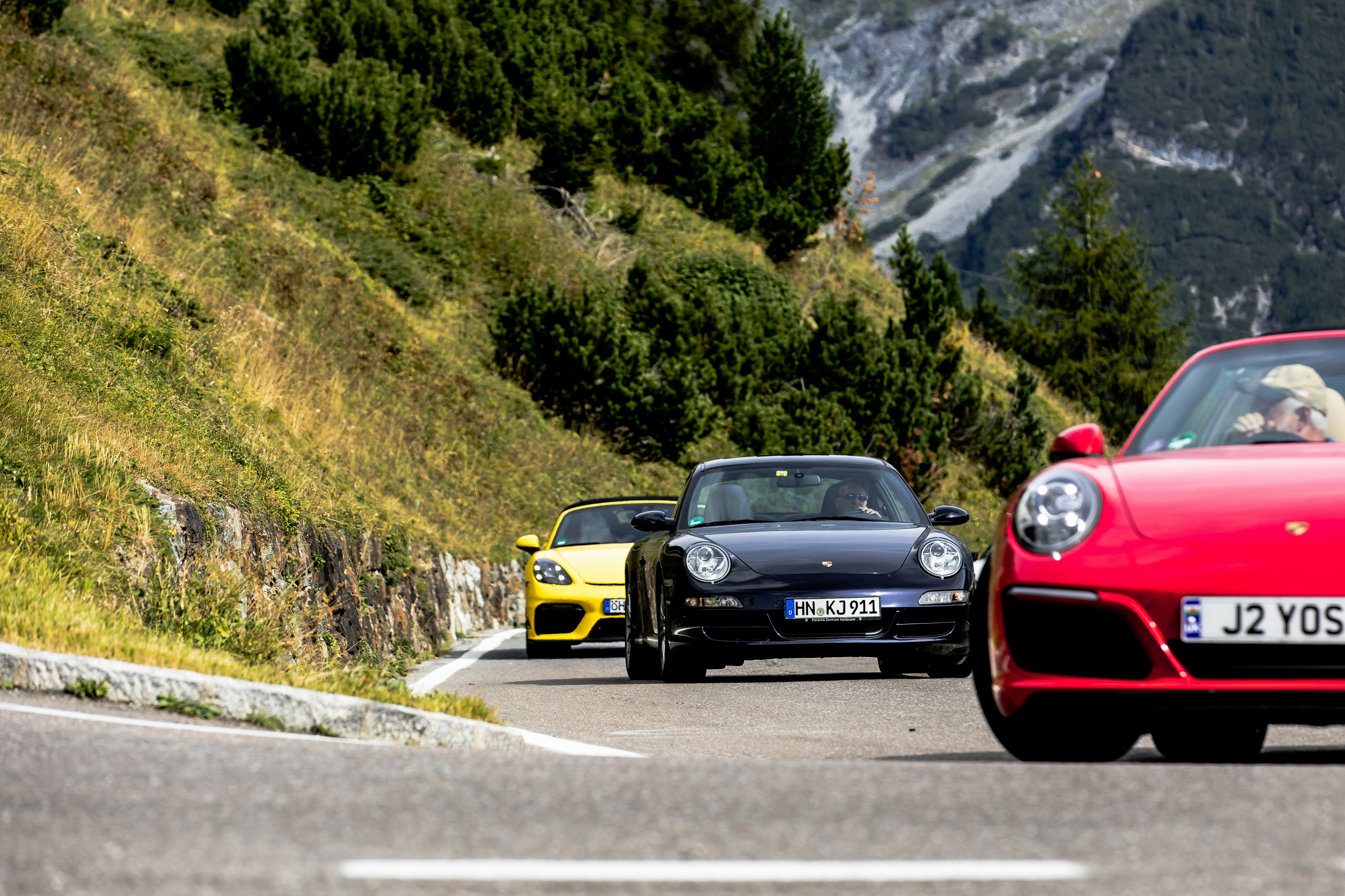 A couple of cars driving down a road next to a mountain photo – Free ...