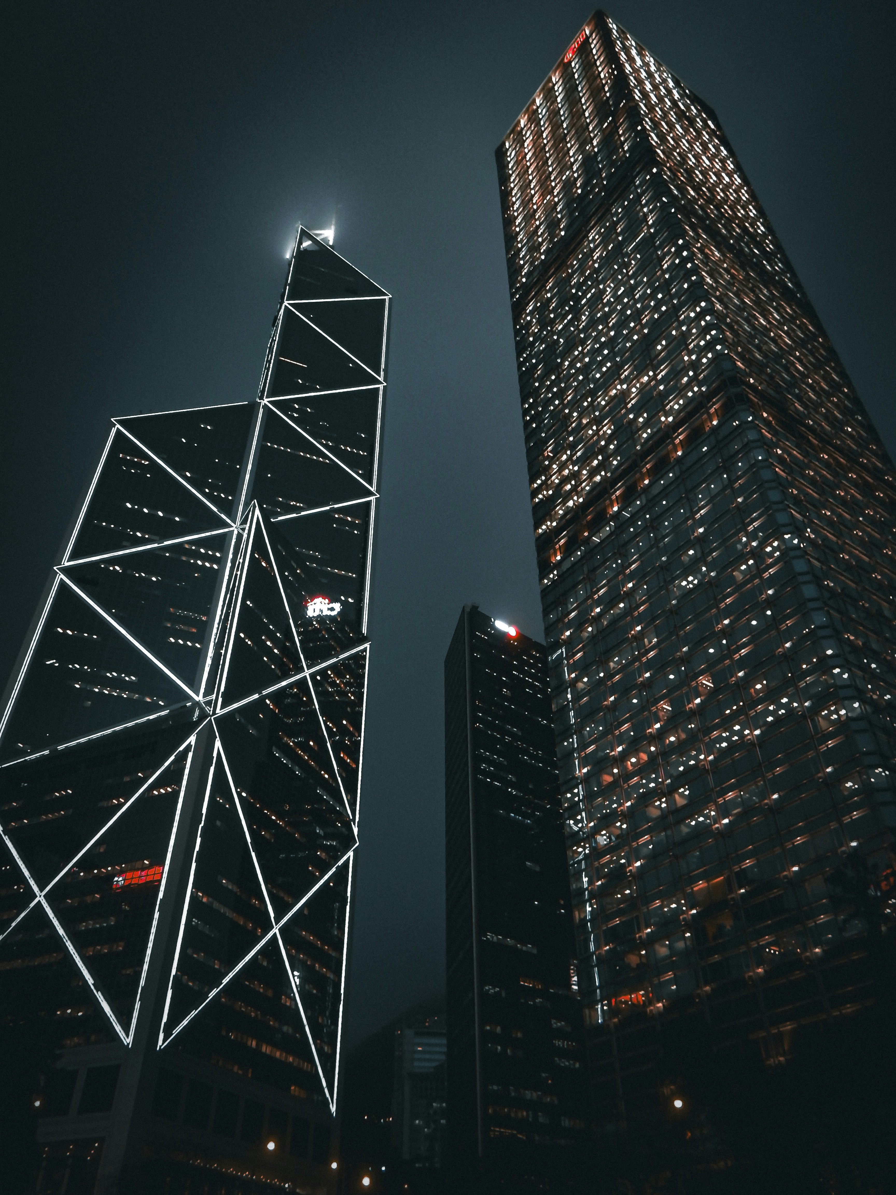 Night cityscape photograph featuring a geometric-lit tower and a tall glass-clad skyscraper against a dark sky.