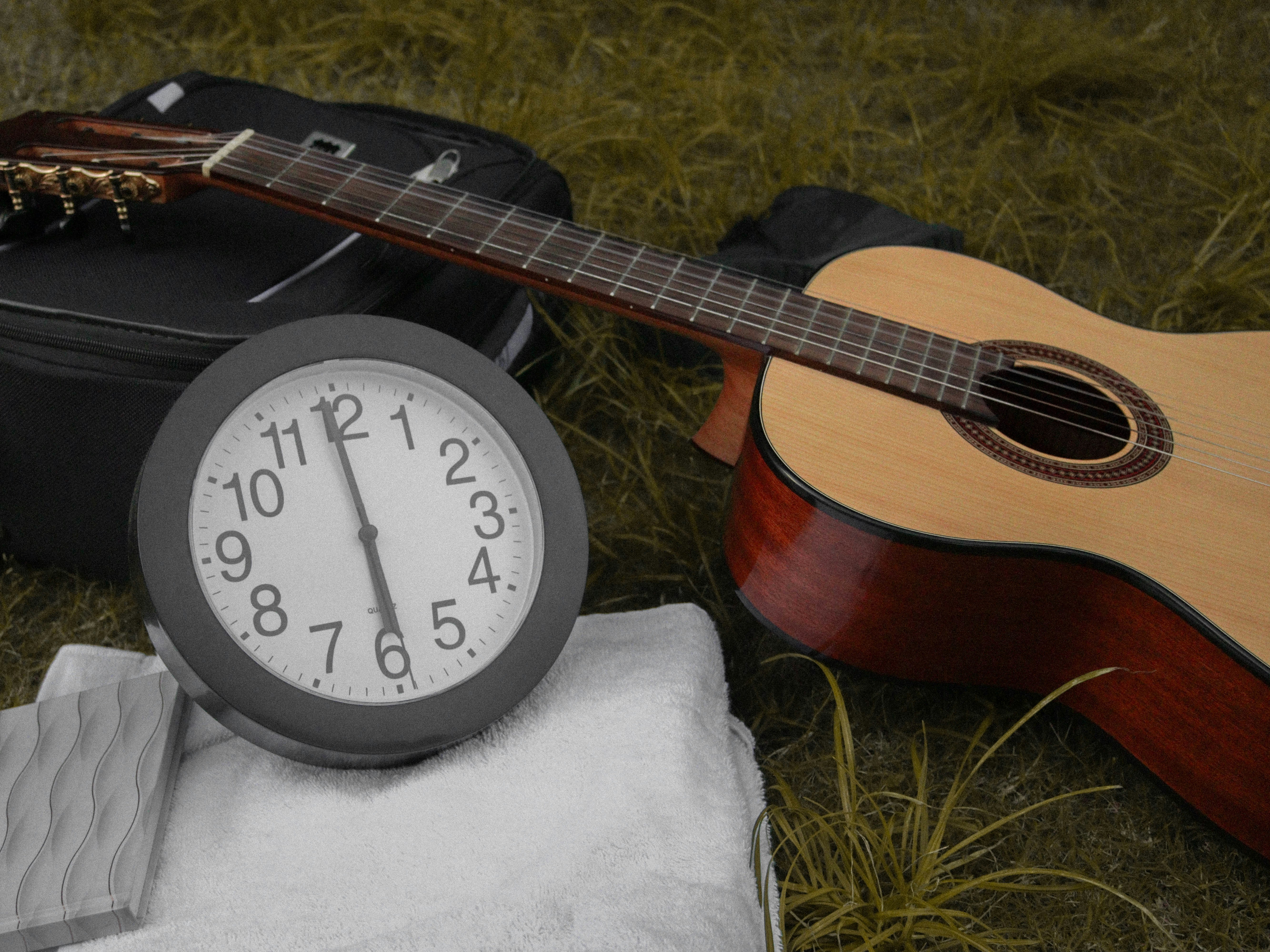Timekeeper Beneath the Strings: A Clock and an Acoustic Guitar Rest on Grass