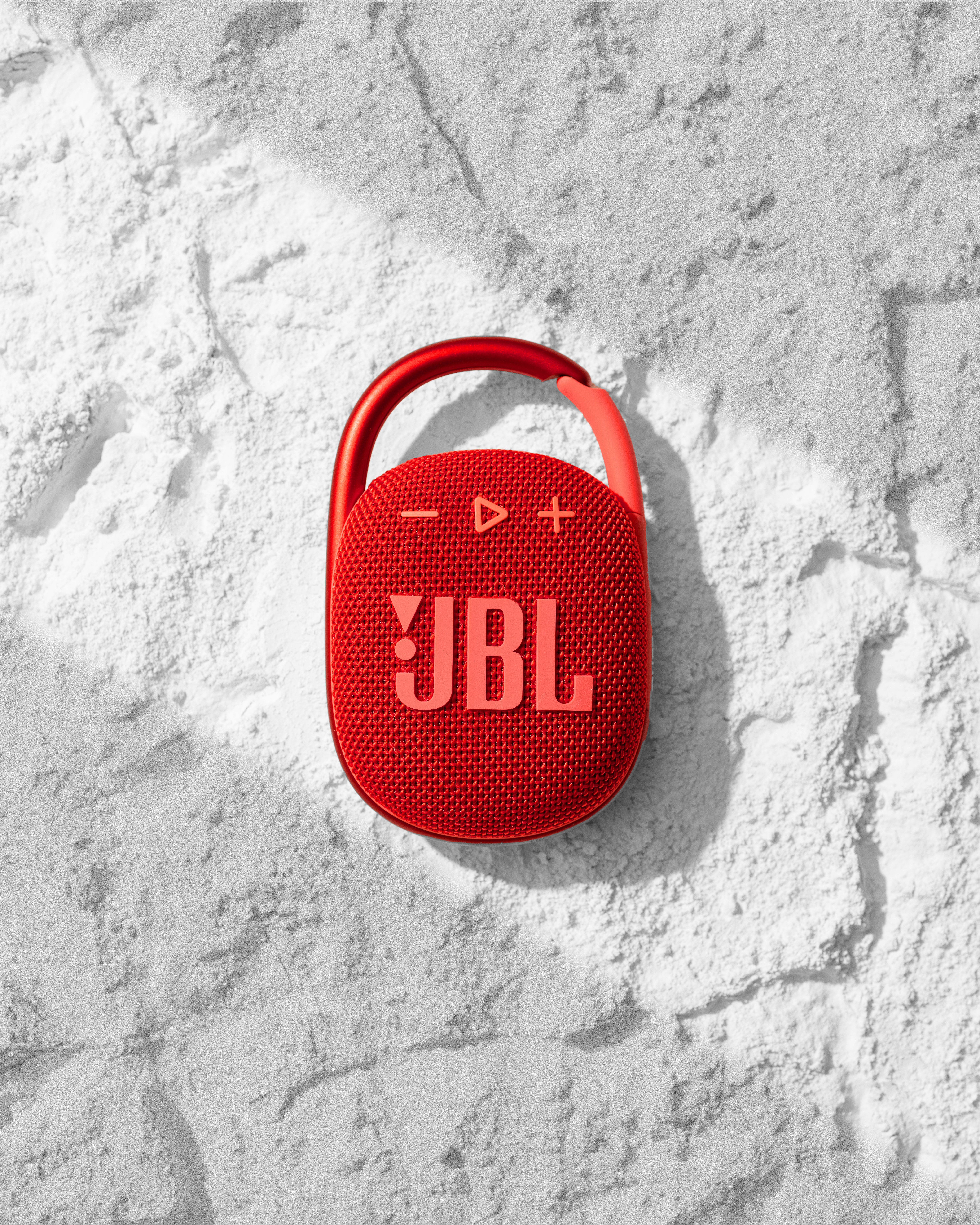 A bright red JBL portable speaker rests atop a textured white surface, showcasing its sleek design and user-friendly controls.