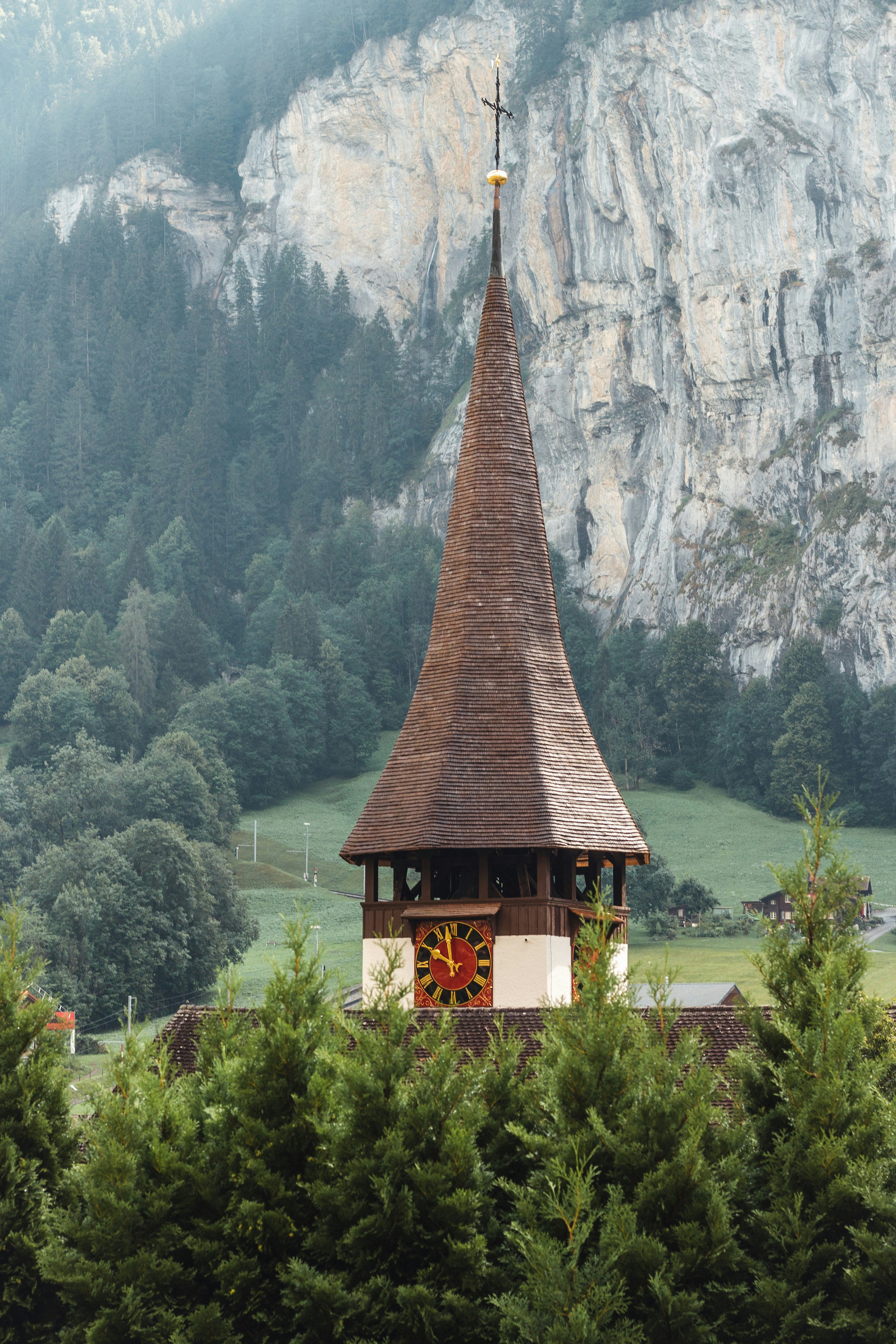 Timber-Spire Clocktower Rising Beneath Alpine Cliffs