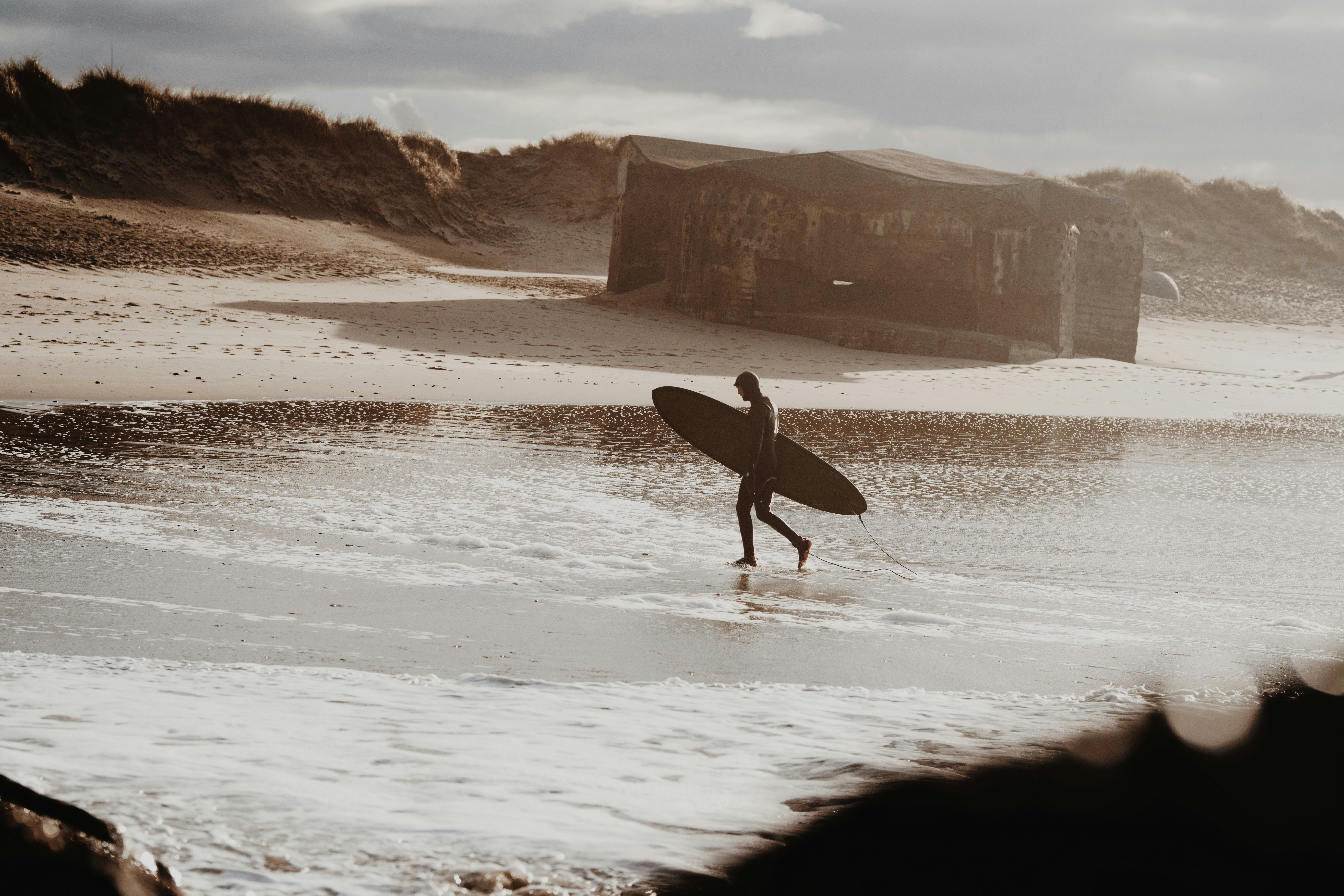Surfer and Surfboard Stride Through Dappled Coastal Light