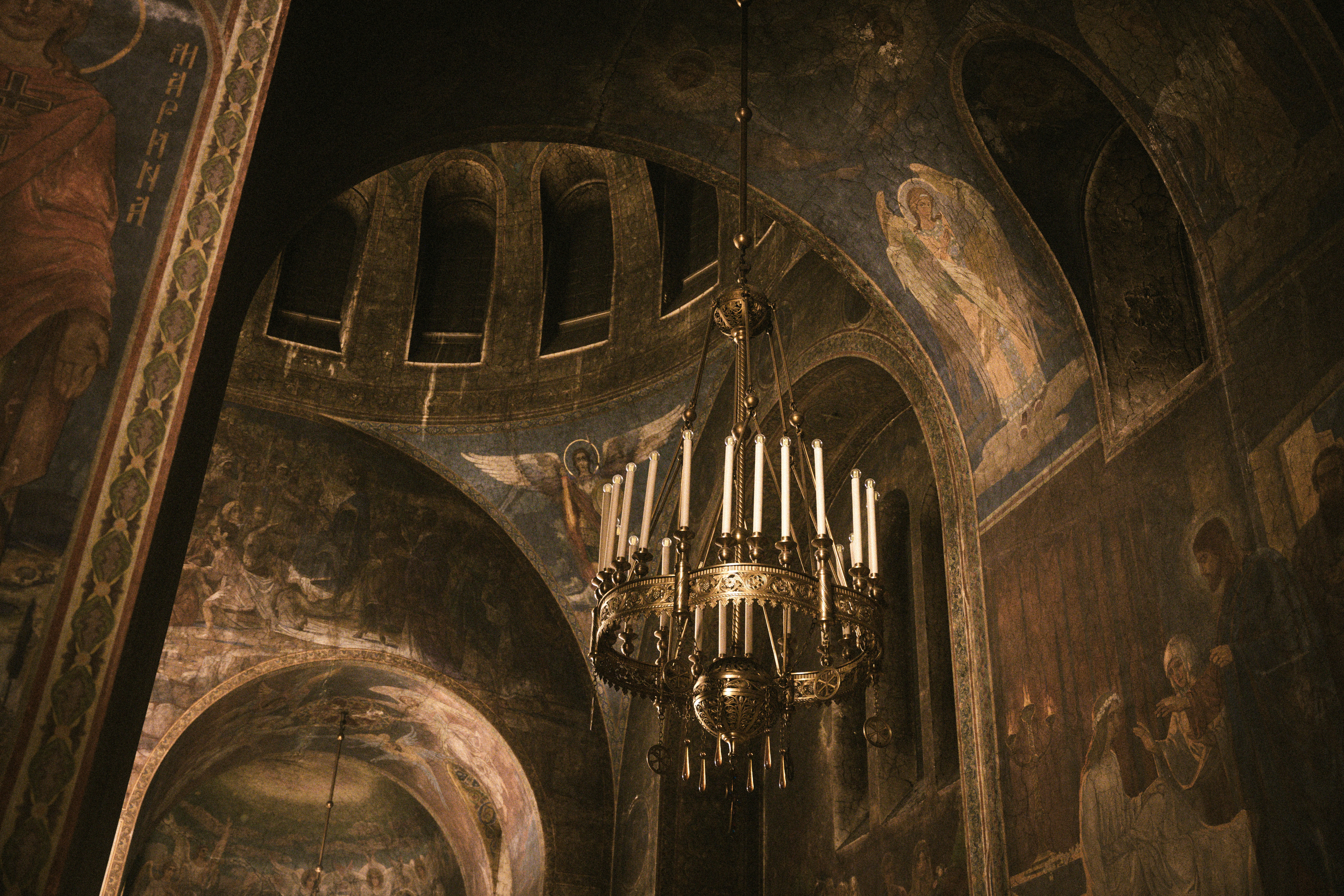 Ornate chandelier illuminating aged cathedral arches with frescoes.