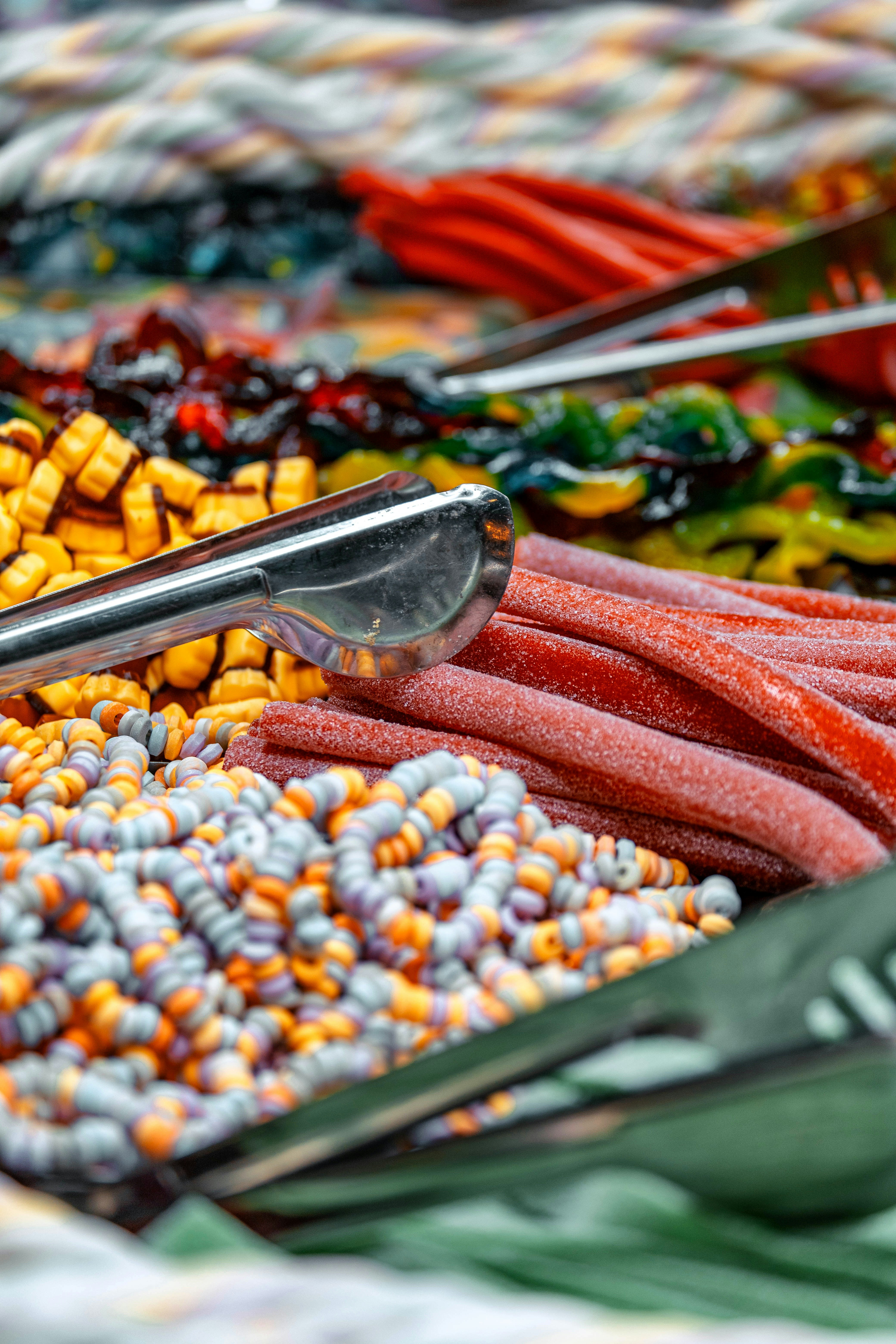 Assorted candies and sweets with tongs at a market stall.