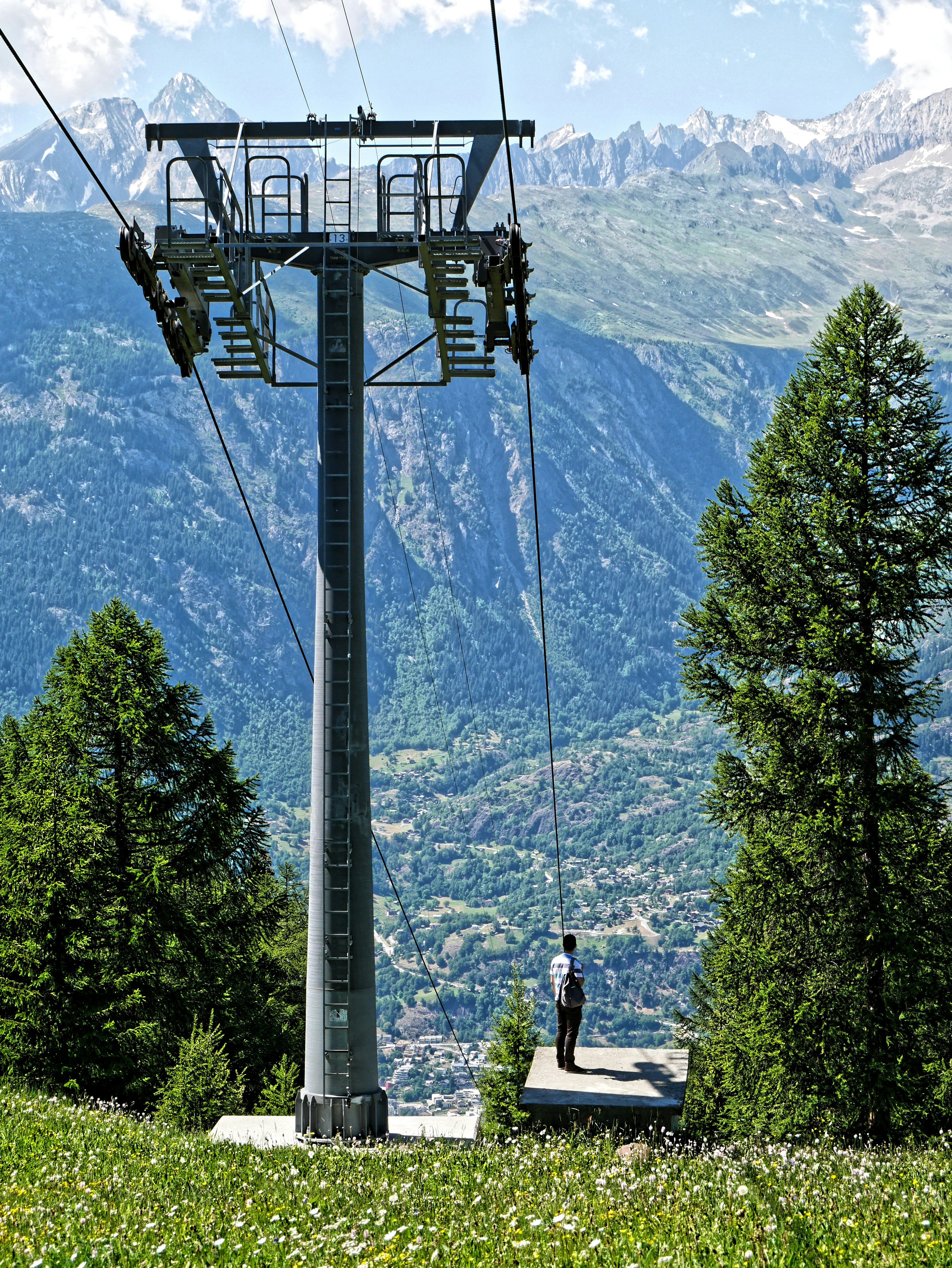 Alpine Lift Sentinel: A lone hiker beneath steel against a mountain panorama