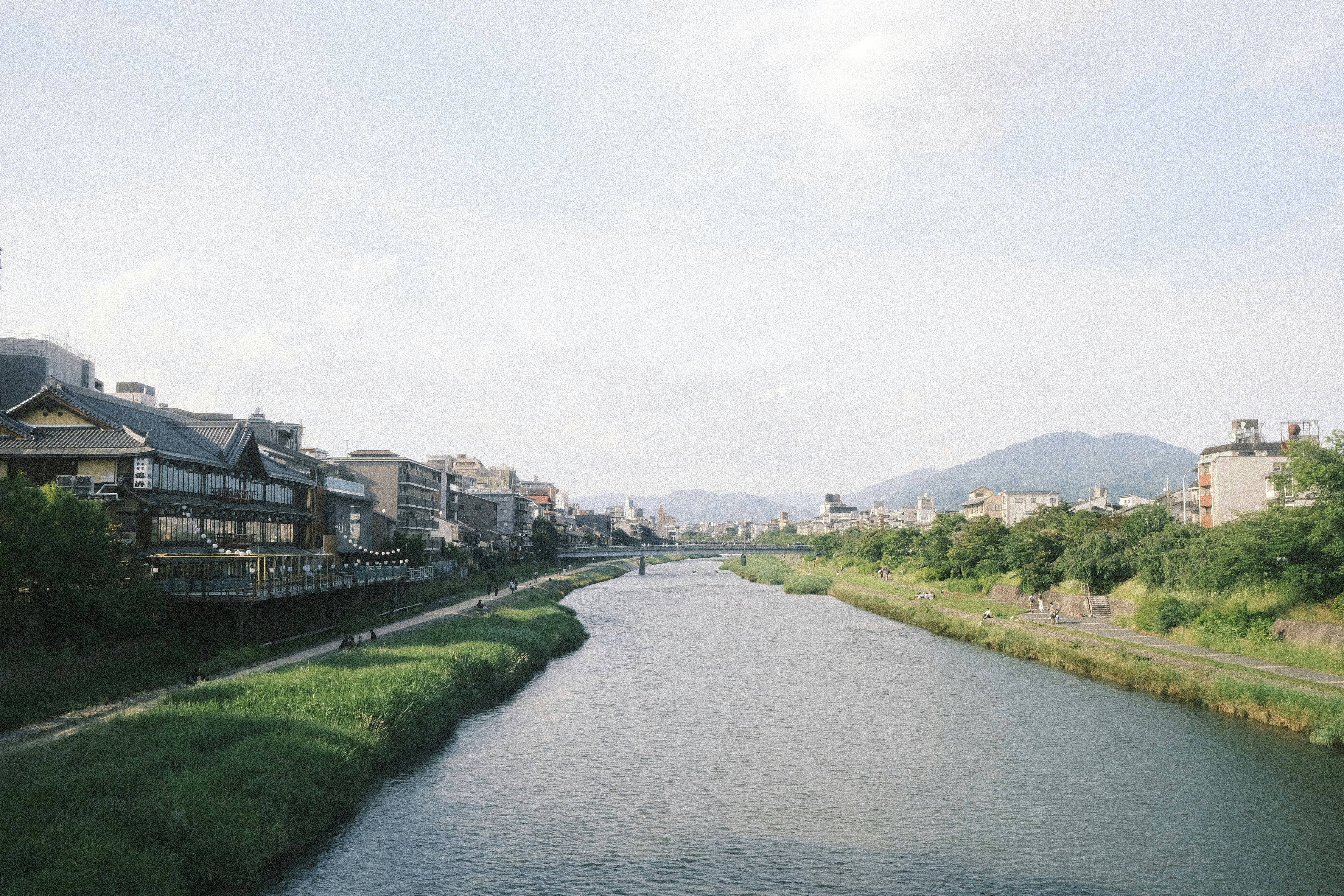 Riverside Echo: Wooden Facades and a Distant Bridge Framed by Hills