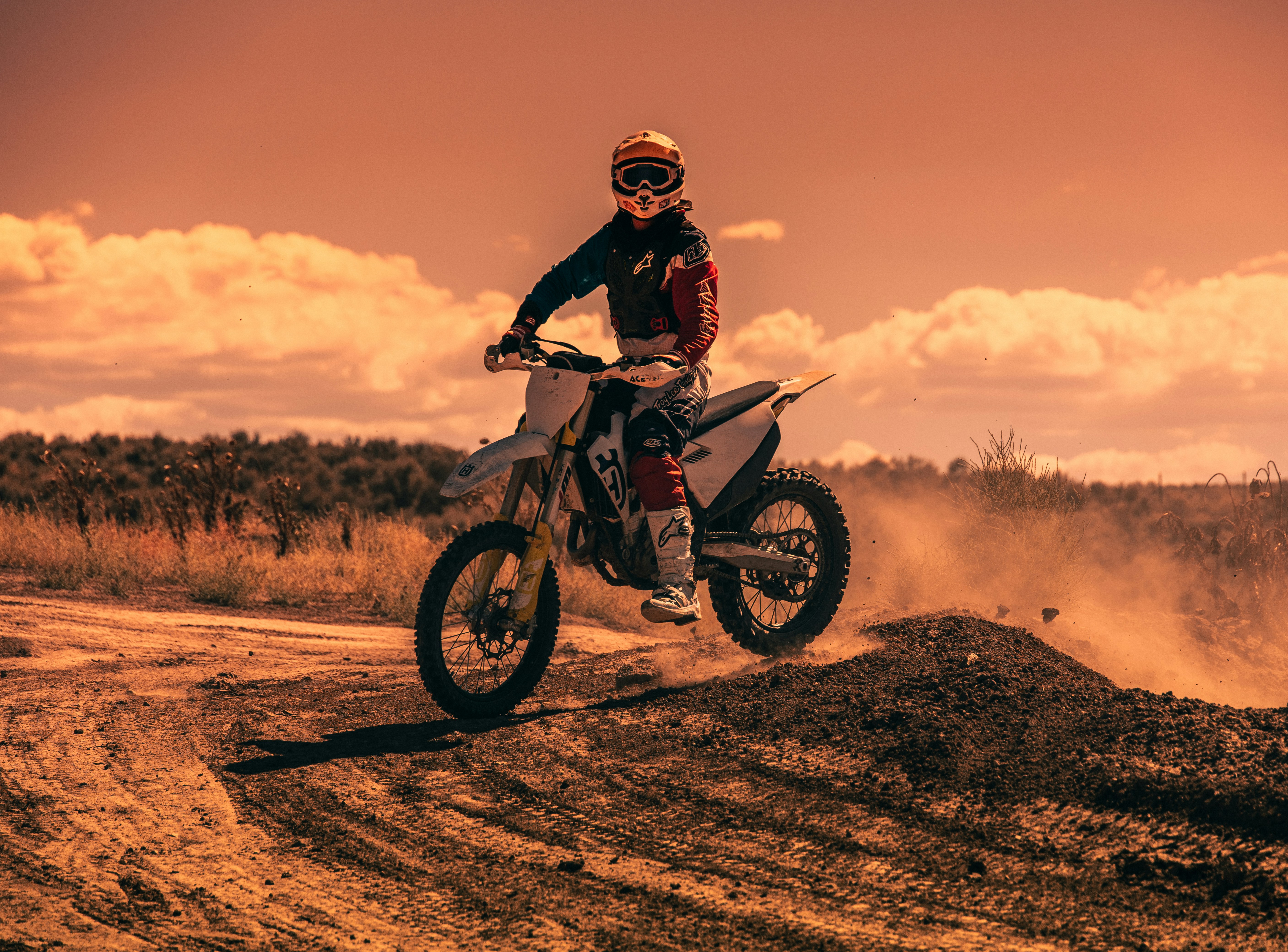 Motocross rider navigating a dirt track, kicking up dust against a backdrop of dramatic clouds and warm tones.