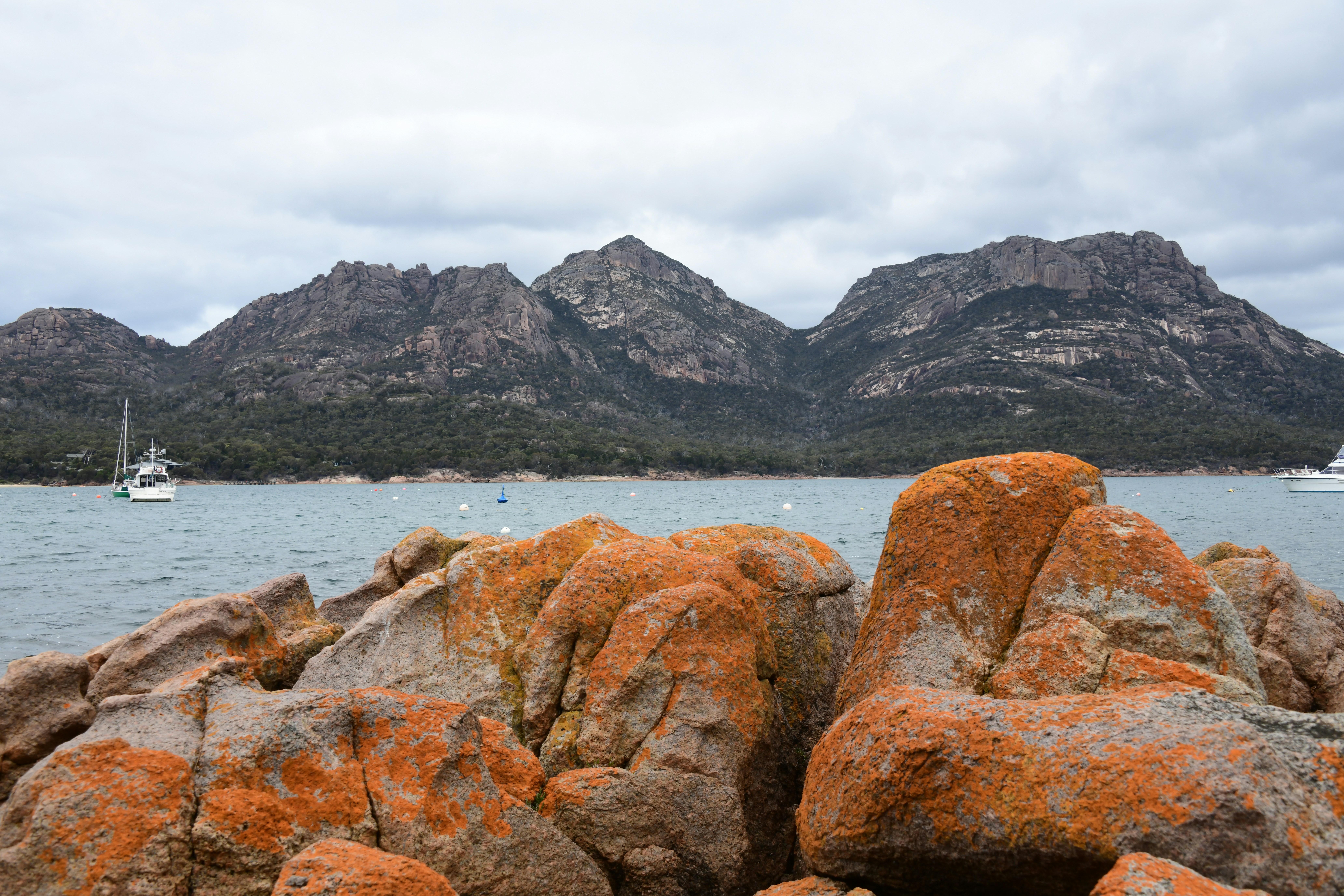 Orange-battered rocks and distant mountains by a calm sea