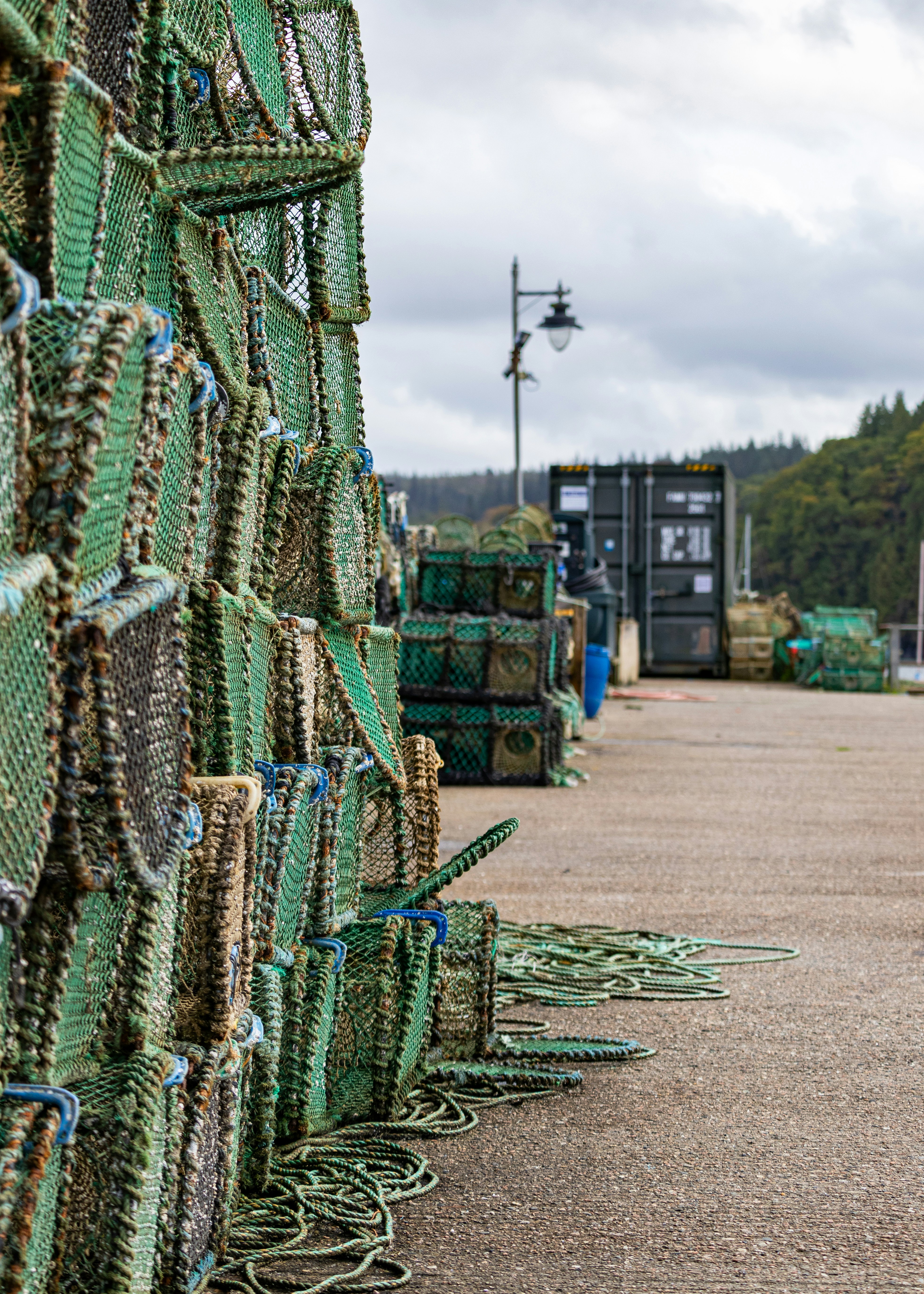 Harbor's Green Fortress: Stacked Lobster Traps Along a Quiet Wharf