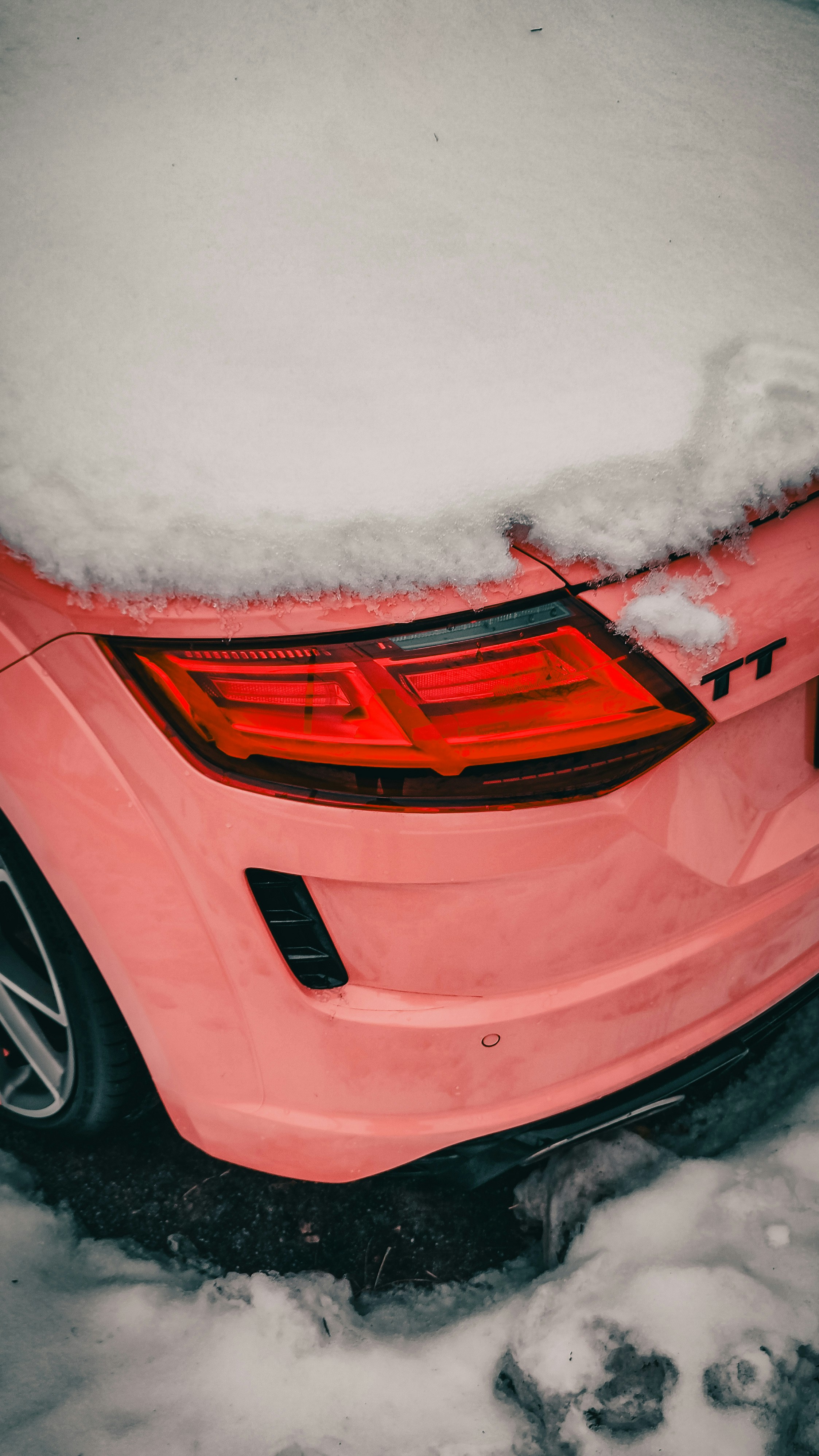 Close-up of a pastel pink car tail light and rear bumper covered in snow. The frame emphasizes winter contrast and automotive design details.