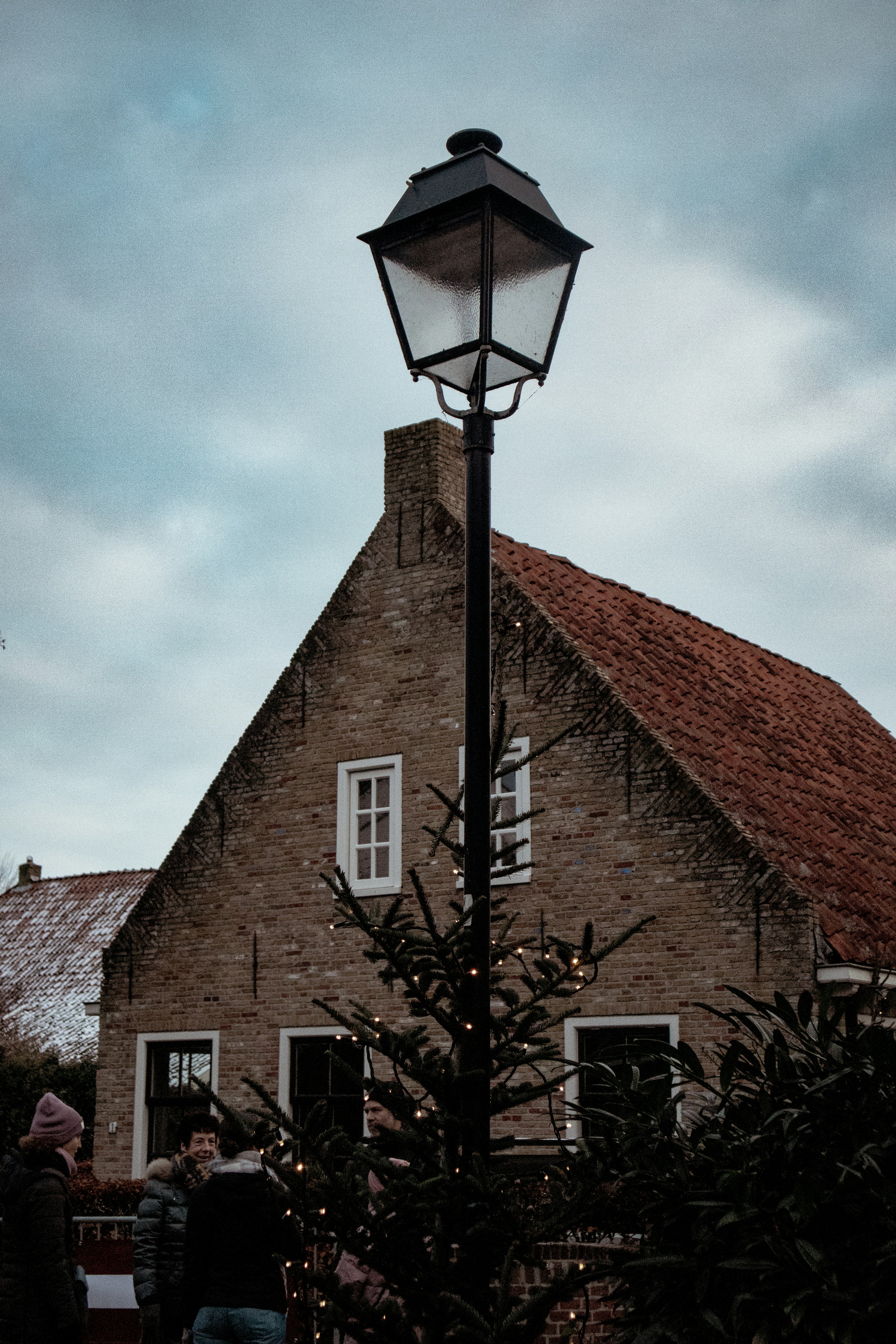 Lamp-Top Lantern Framing a Brick Gable in a Dusk Christmas Lane