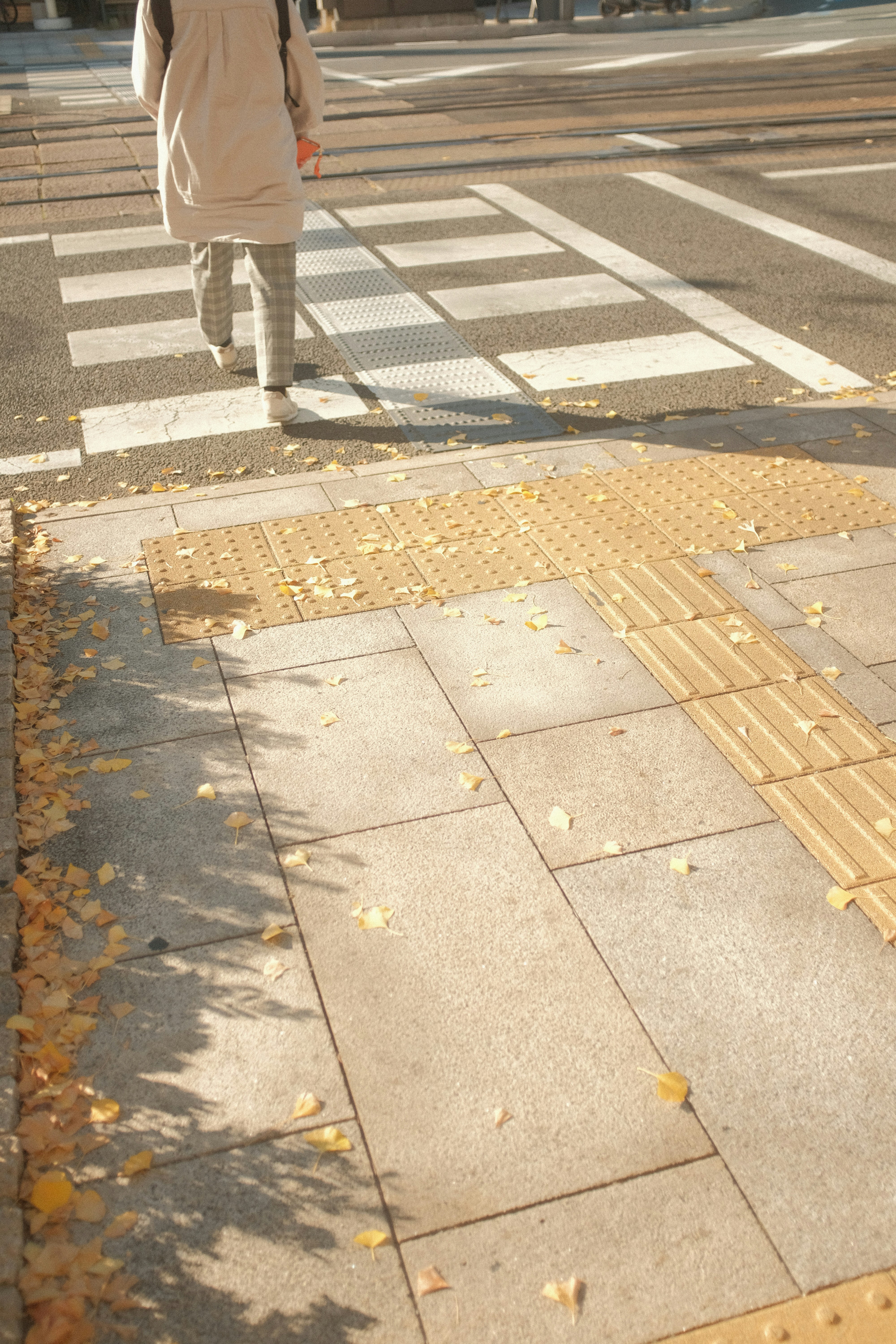 Sunlit Crossing: A Beige-Coat Pedestrian Traverses a Quiet City Crosswalk