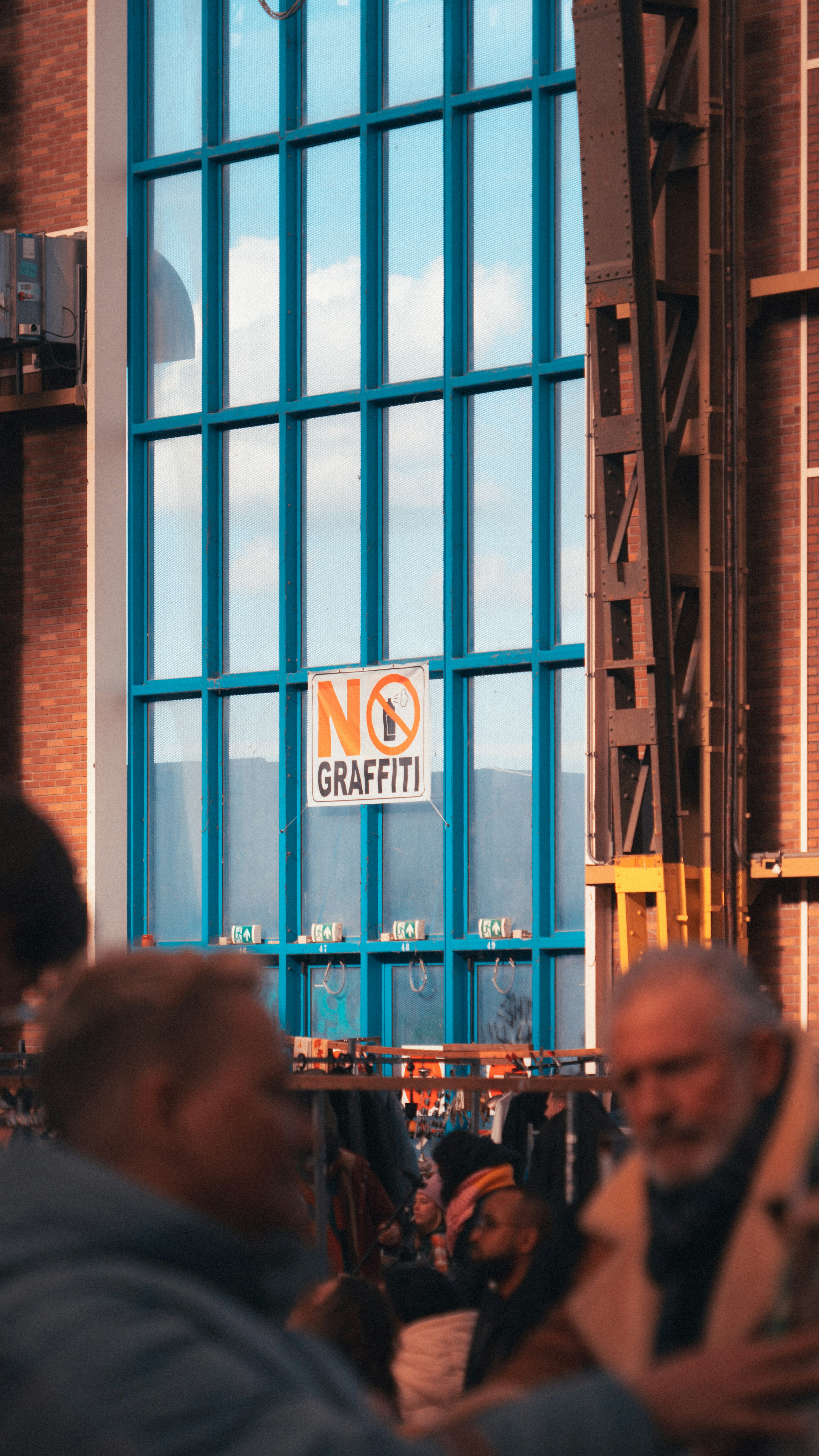 No Graffiti Sign Framed by a Blue Glass Grid in a Busy Urban Moment