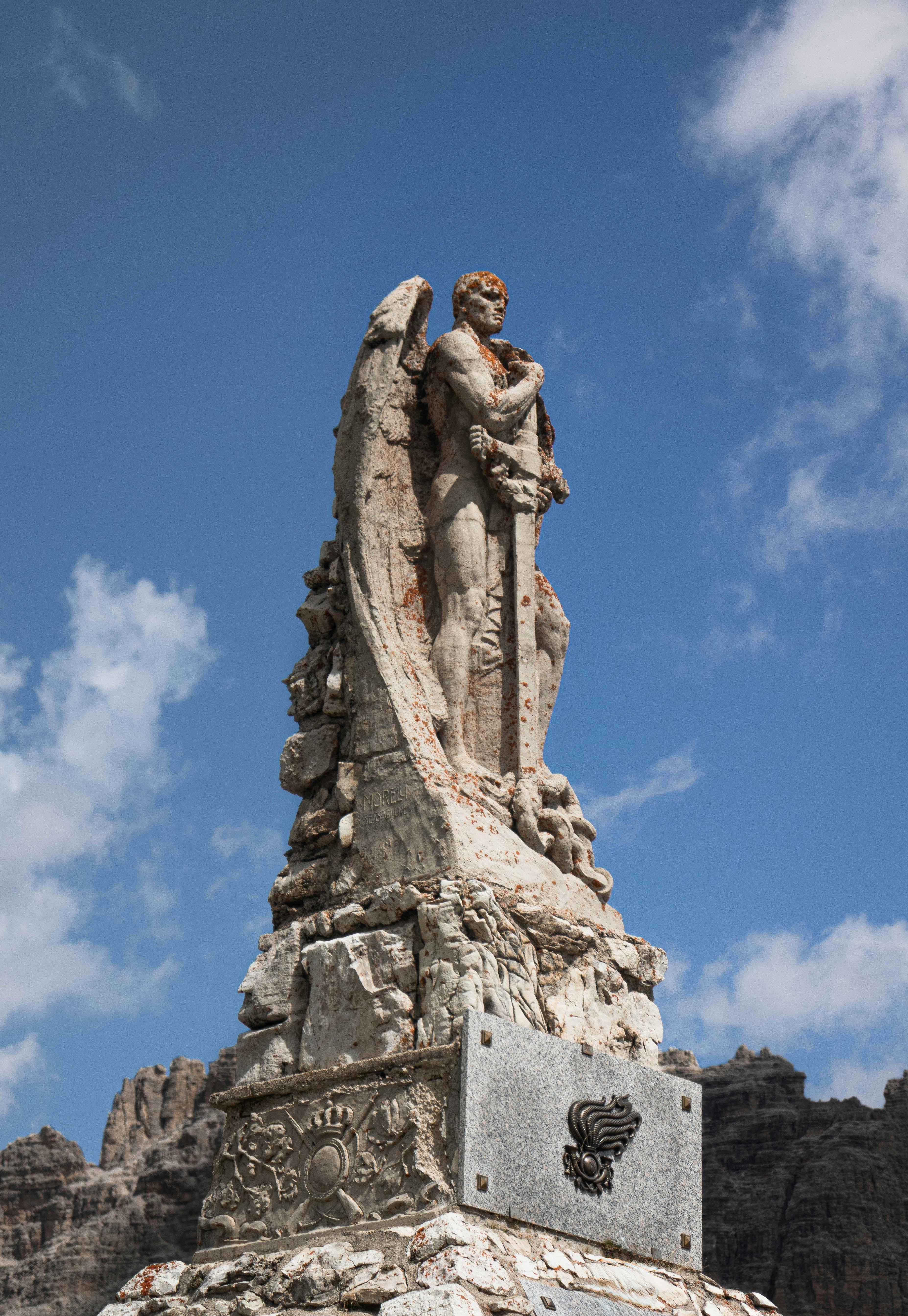 Stone Sentinel: Angel Rising from a Weathered Pedestal Under a Cerulean Sky