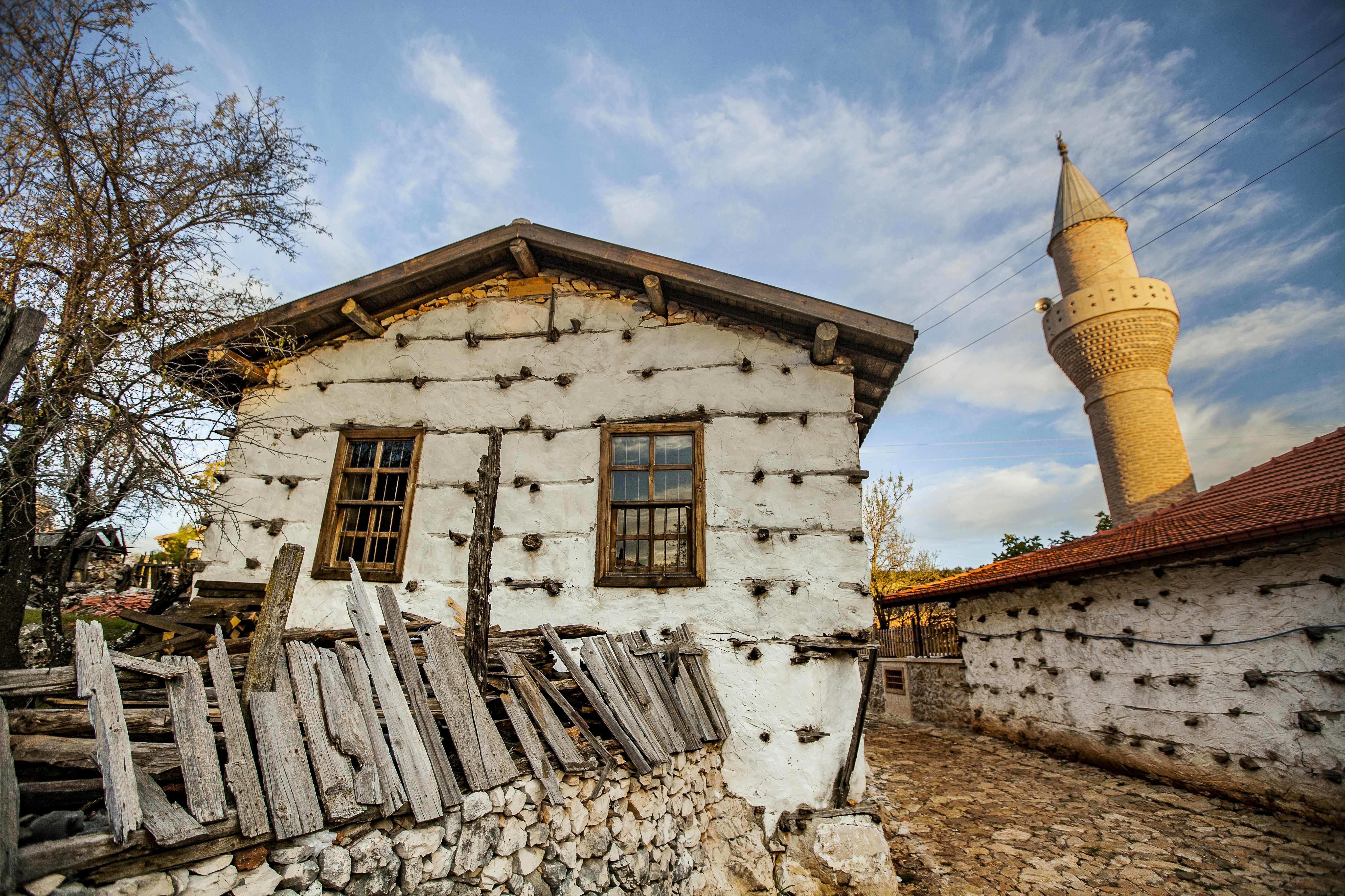White-washed cottage with stacked fencing and a distant minaret under a blue sky