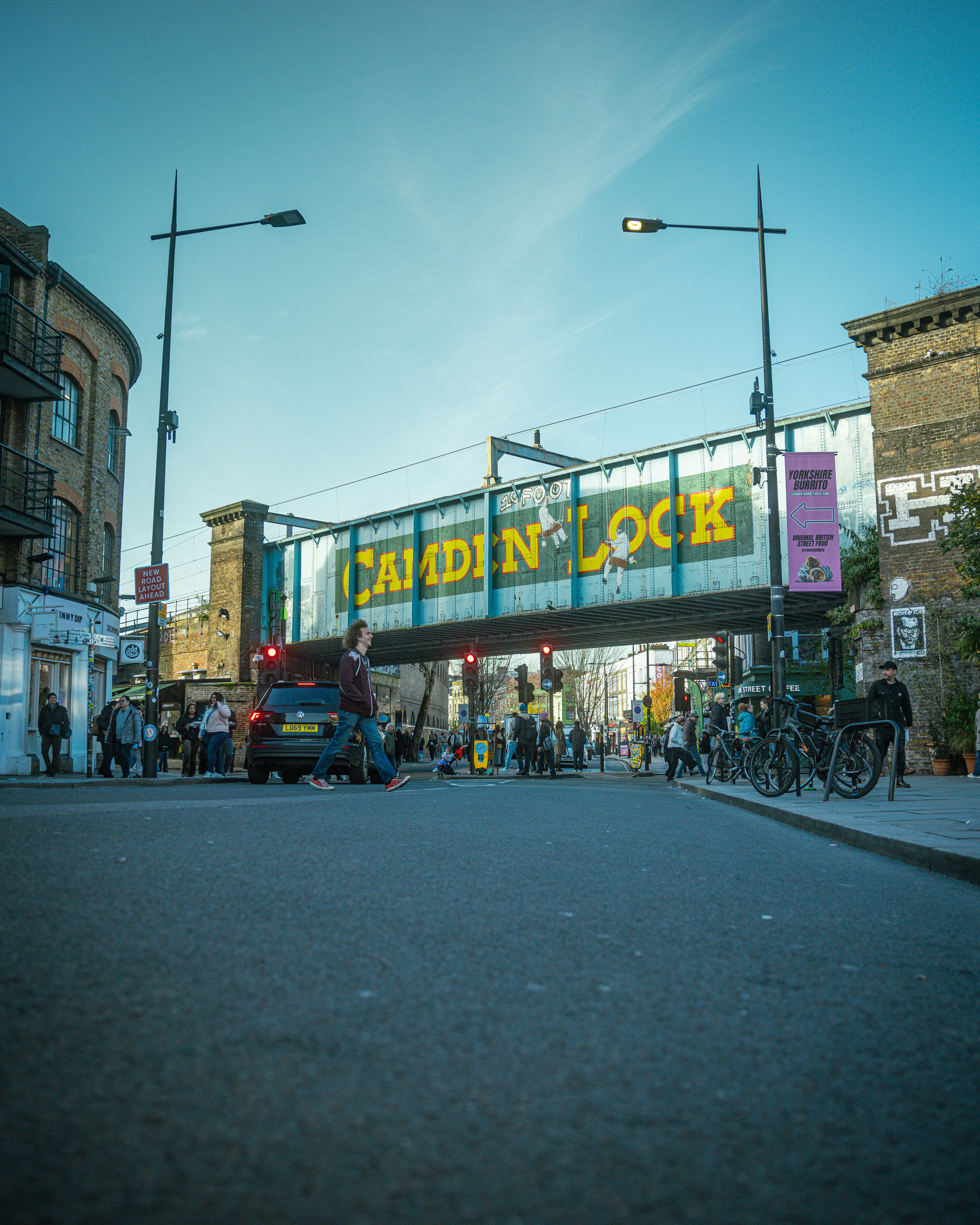 Street-level view of Camden Lock bridge with pedestrians and bicycles under a clear blue sky.