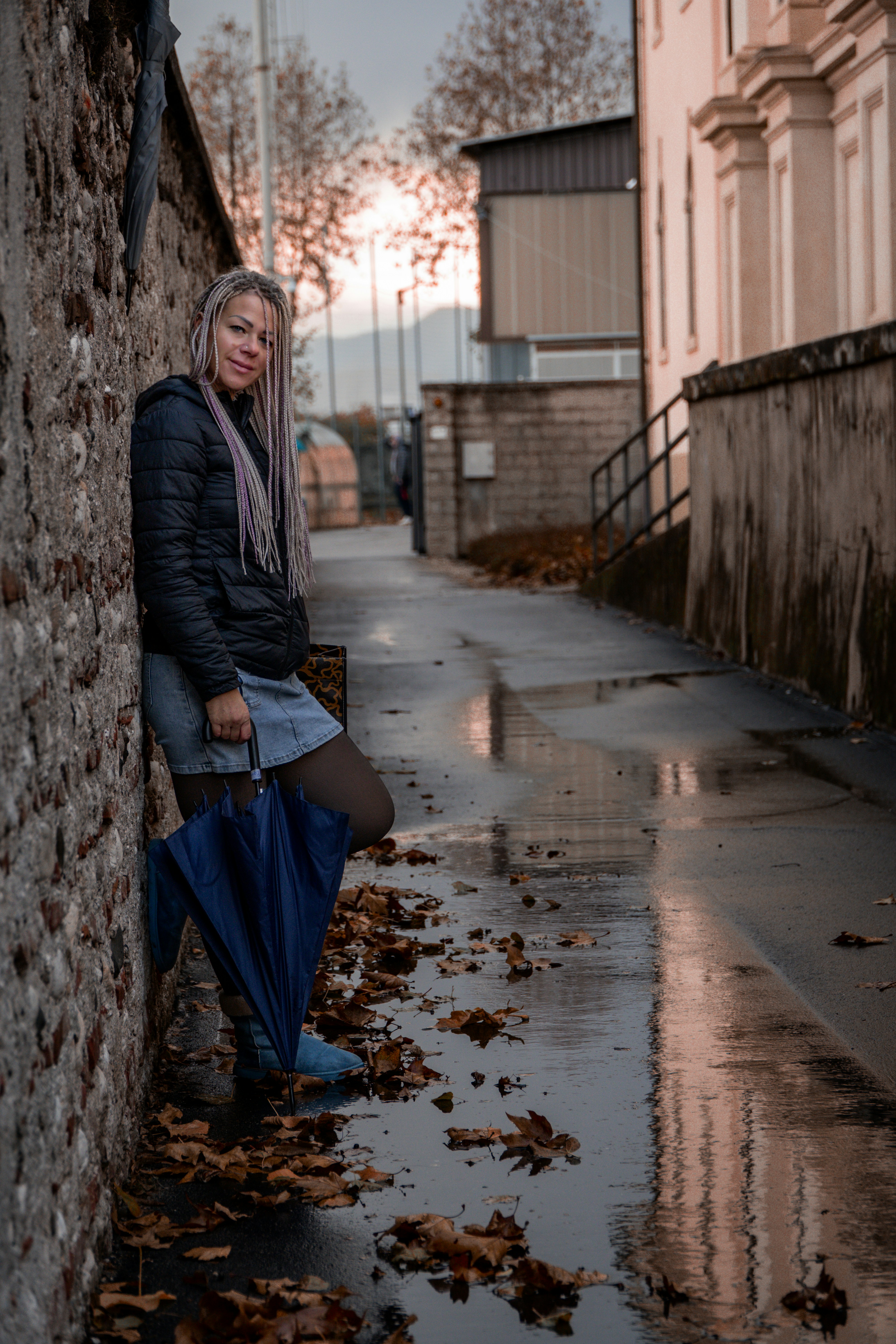 Urban Dawn: a woman in a puffer jacket leans against a mossy wall at sunset