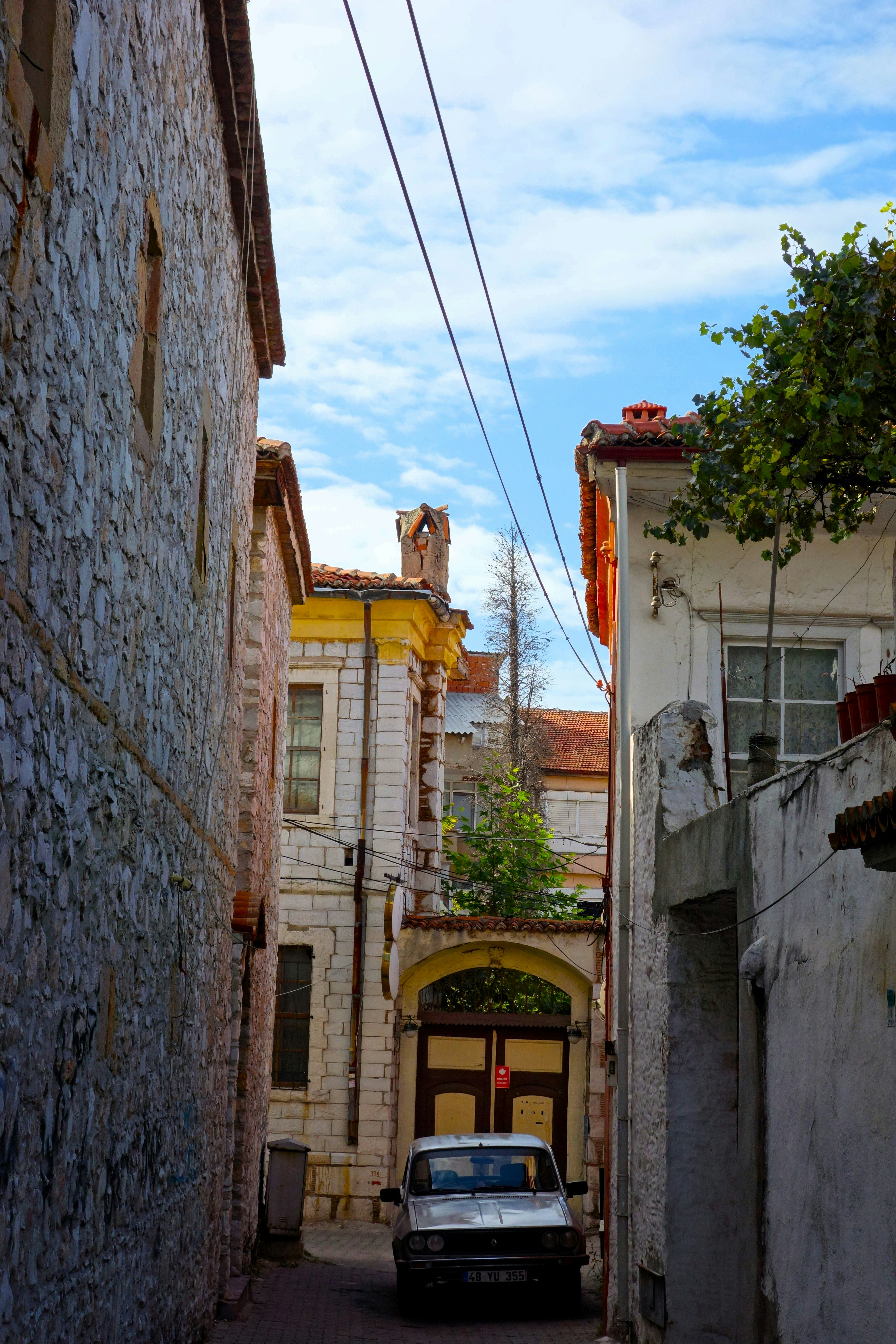 Charming alleyway flanked by textured stone walls, leading to a glimpse of a quaint building and a parked car. The scene evokes a sense of nostalgia.