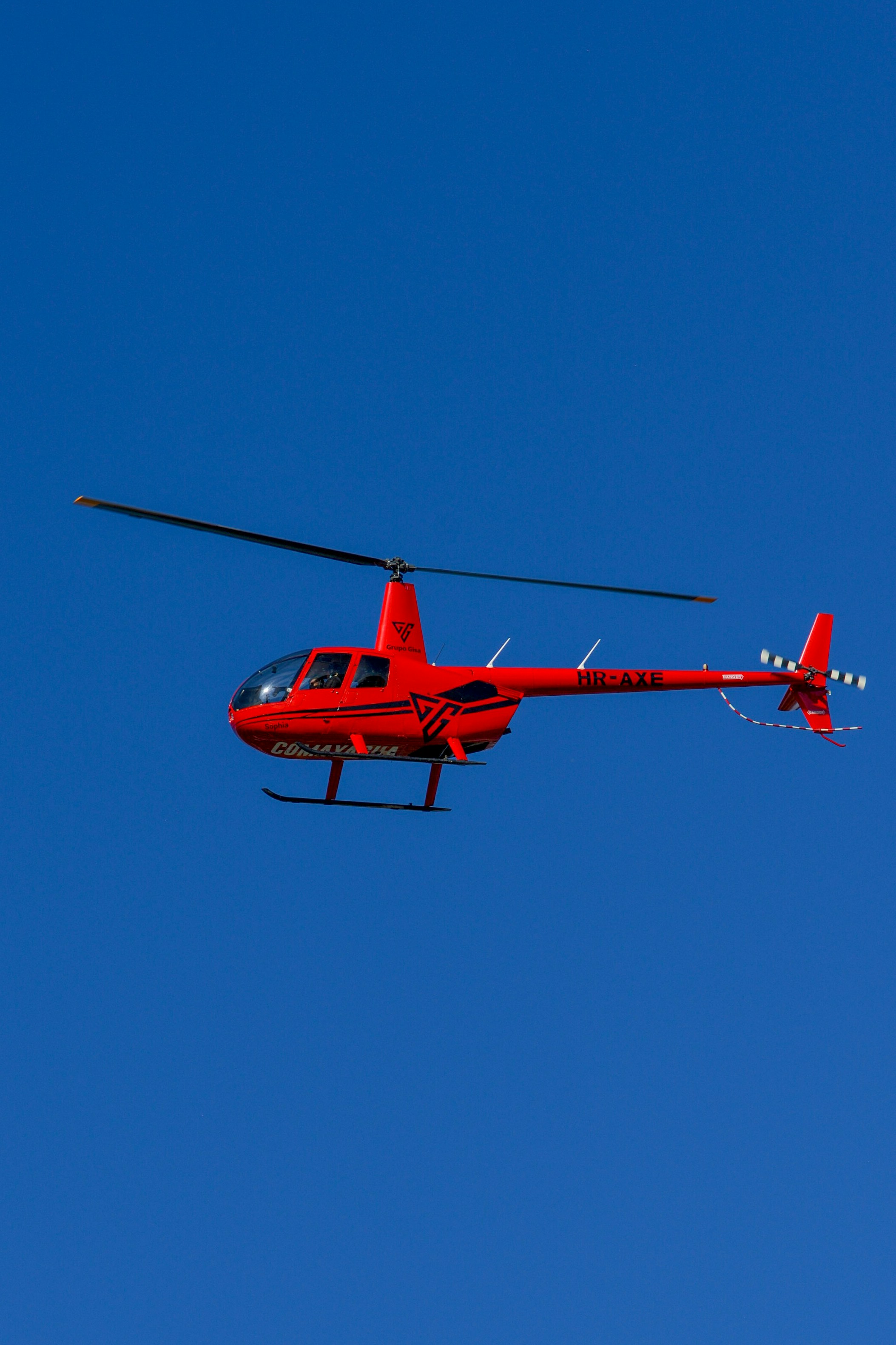 Crimson Courier: Red Helicopter Slices Across a Clear Azure Sky