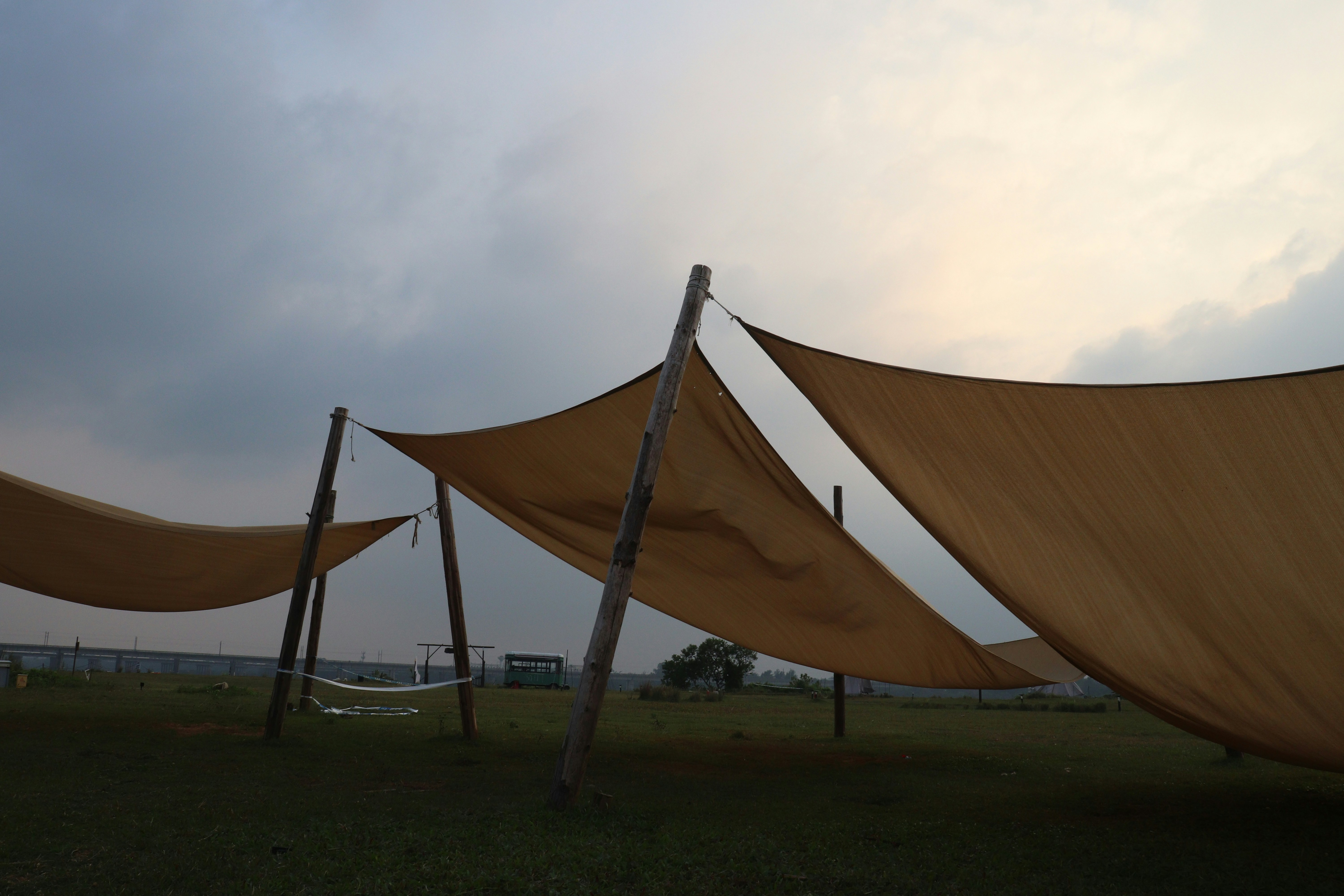 Large canvas sheets stretched over wooden poles under a cloudy sky.
