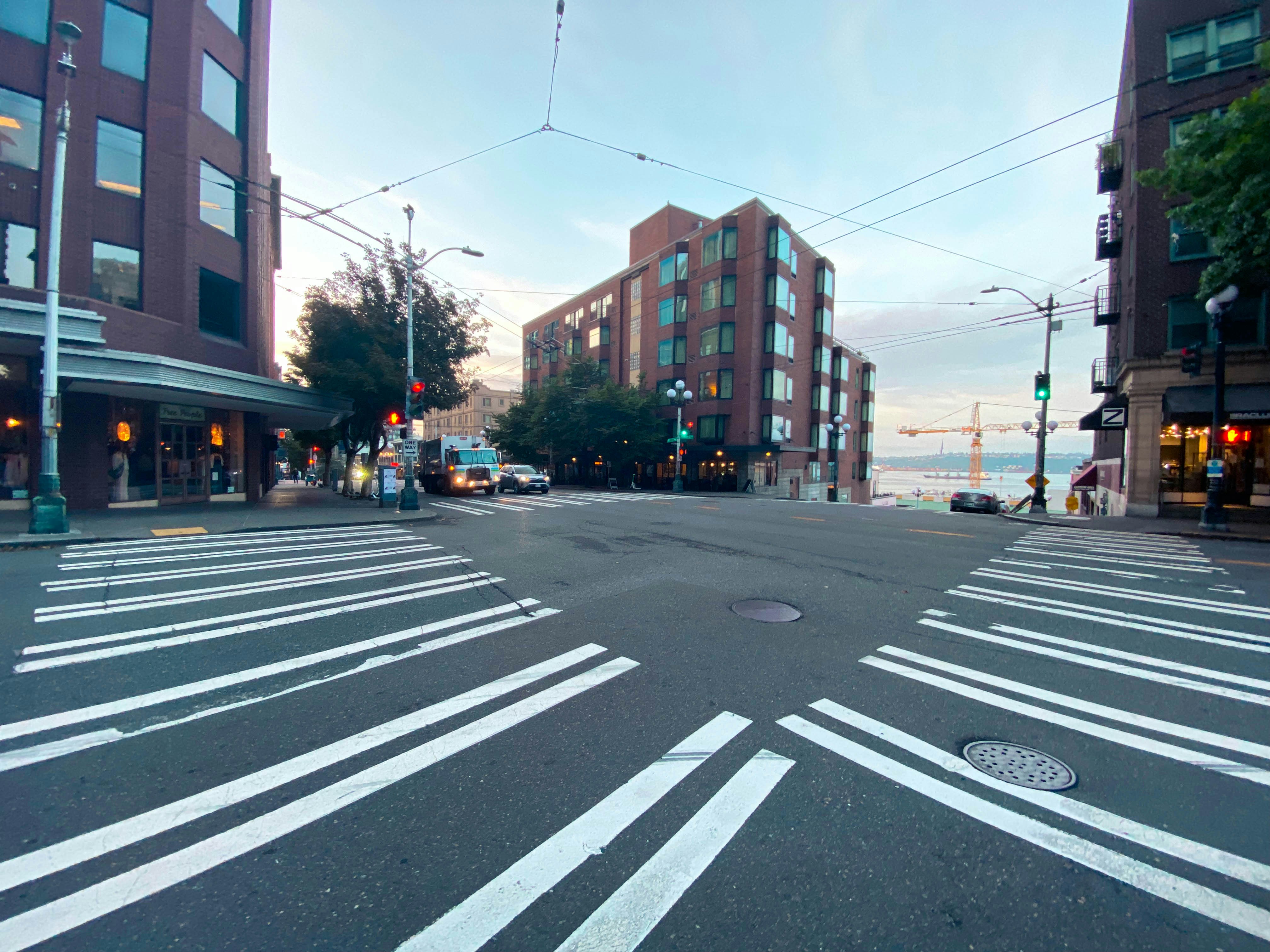 Busy urban intersection featuring distinctive crosswalk lines and modern architecture, with a hint of sunset in the sky.