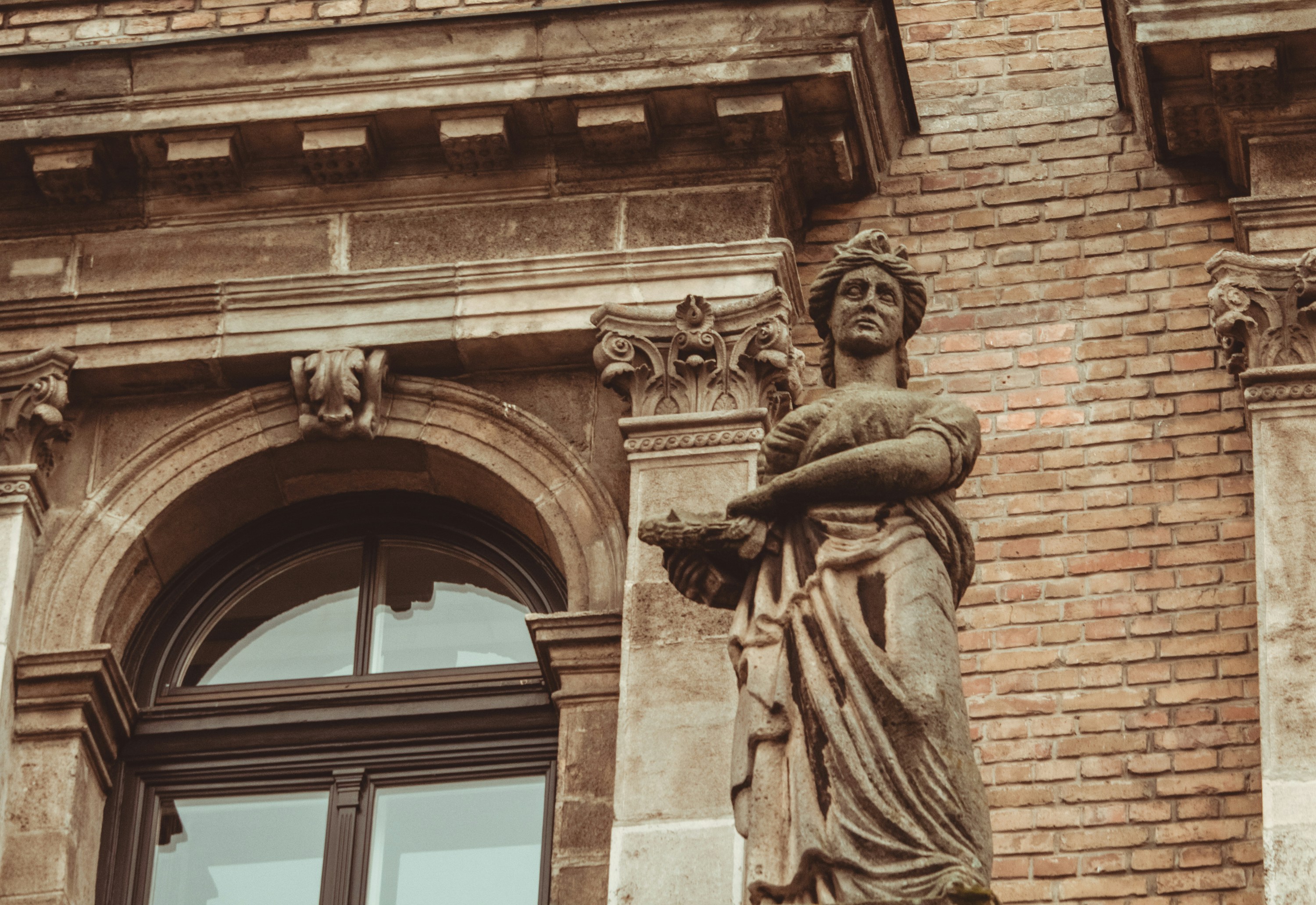 An Old Brick Facade with a Classical Statue Guarding the Arch
